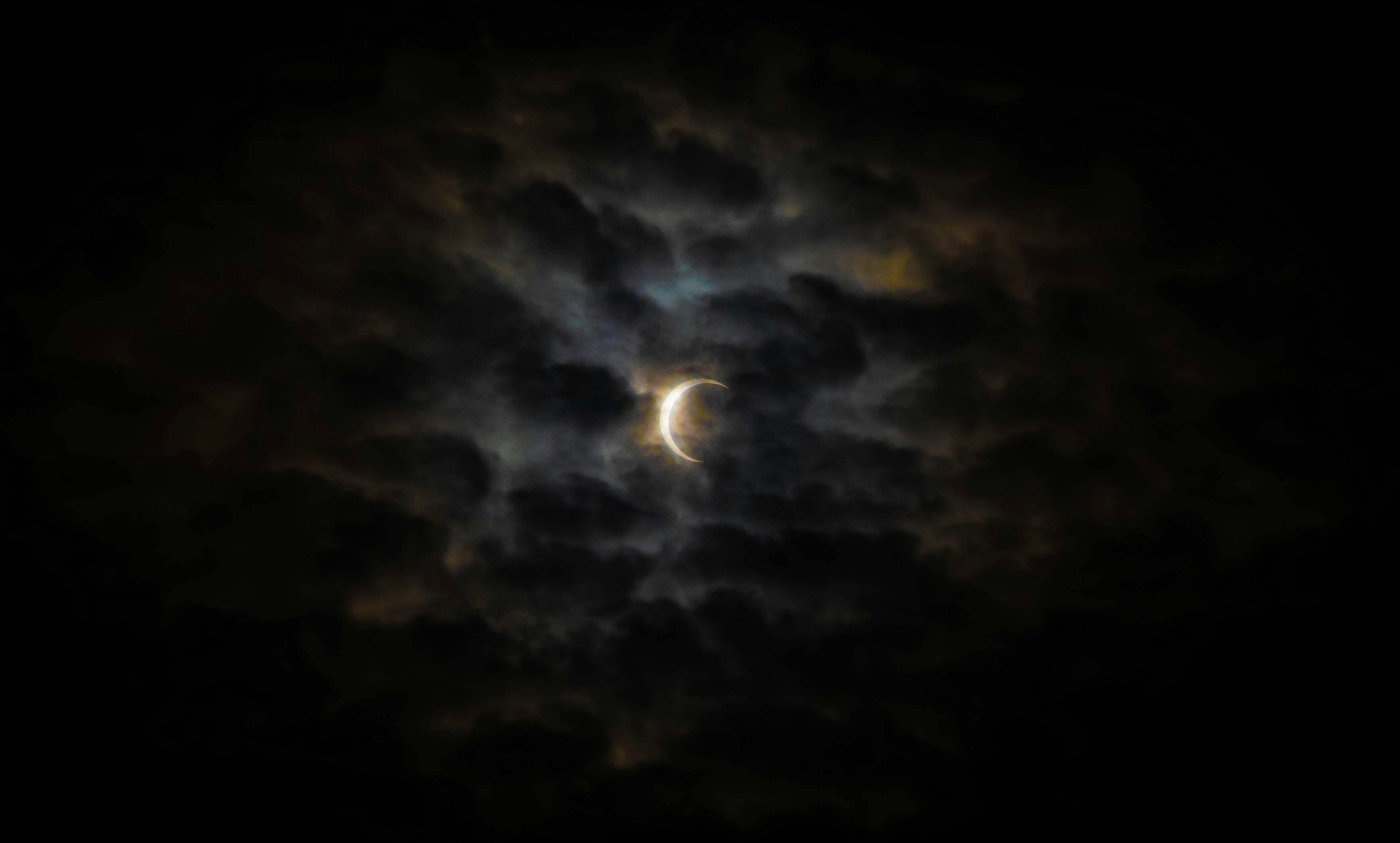 A crescent moon shines through dark, cloudy skies.