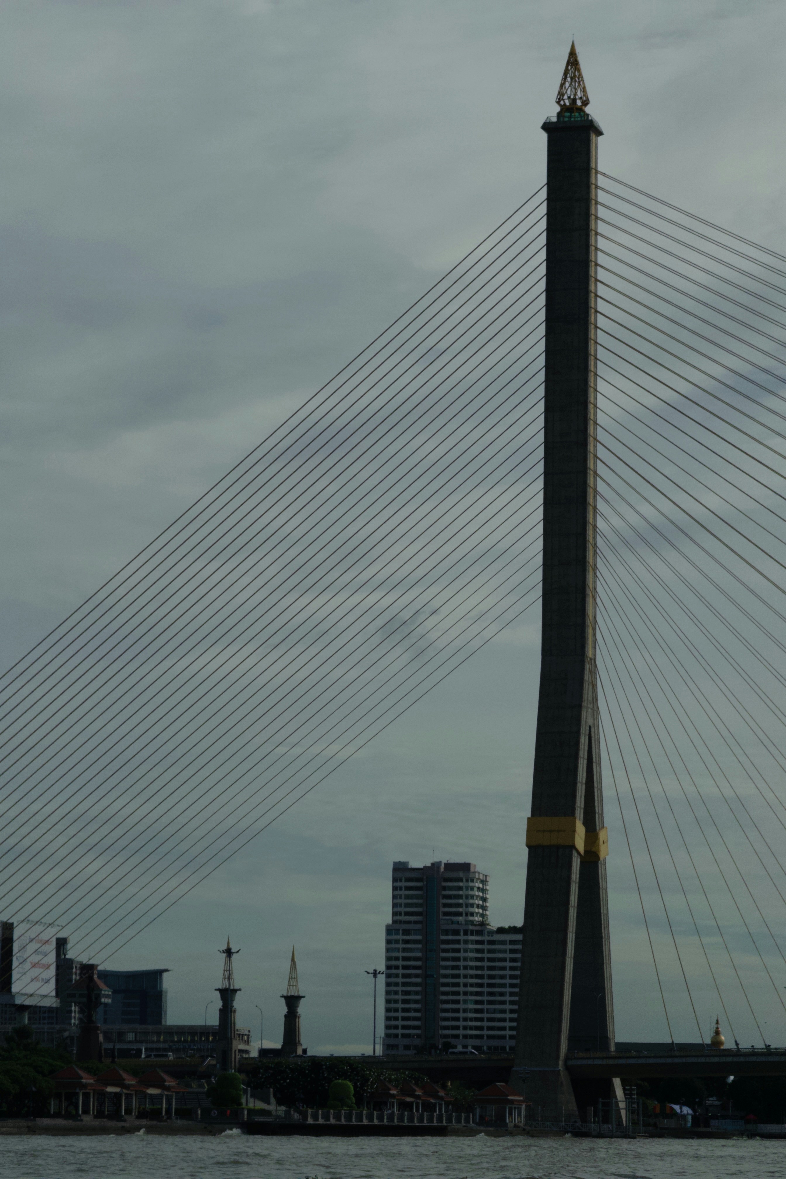 Sleek suspension bridge tower rising majestically against a cloudy backdrop, showcasing modern engineering amidst urban architecture.