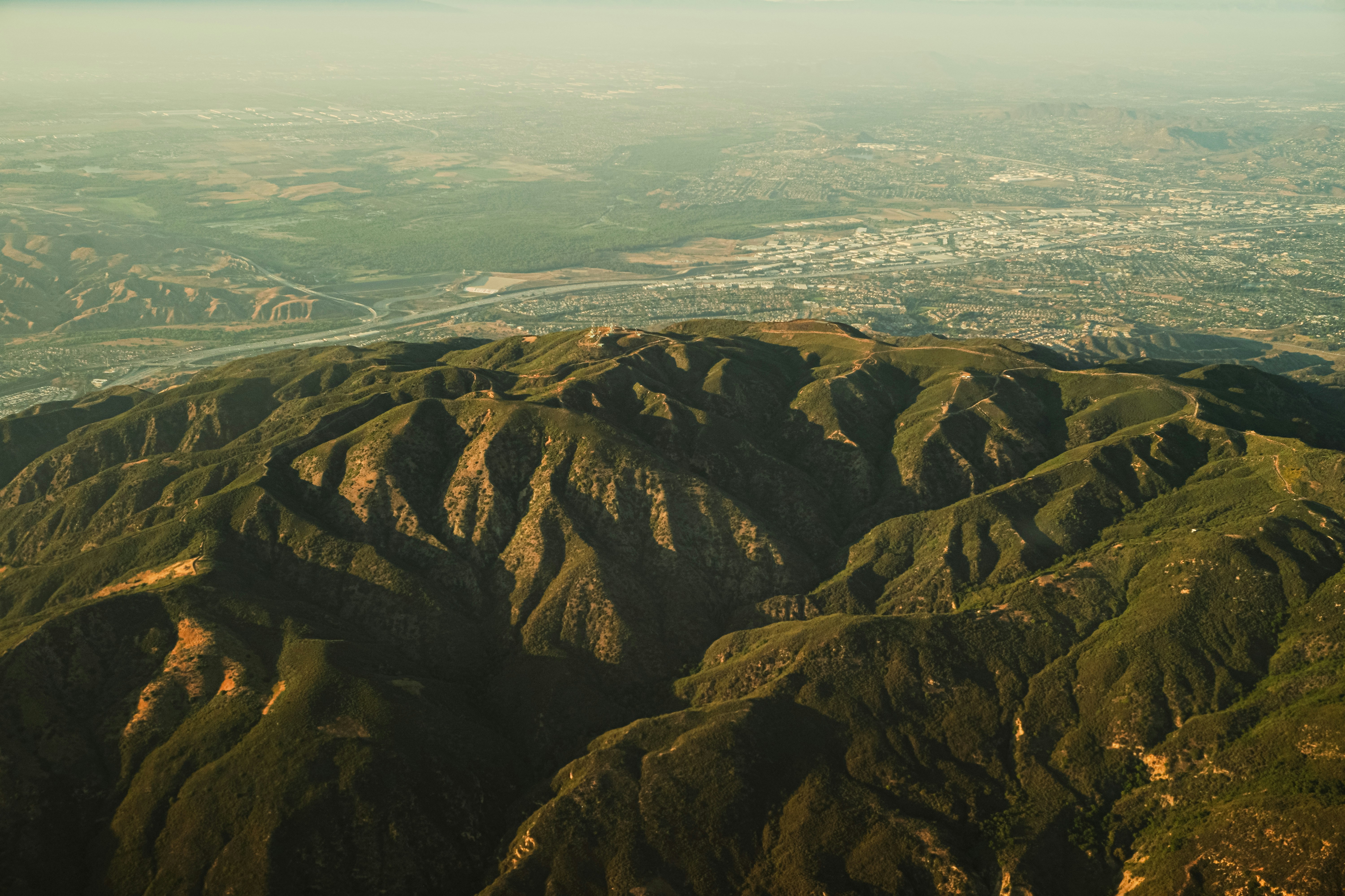 Aerial view showcasing the undulating ridges and valleys of a mountainous landscape, with a distant cityscape visible below.