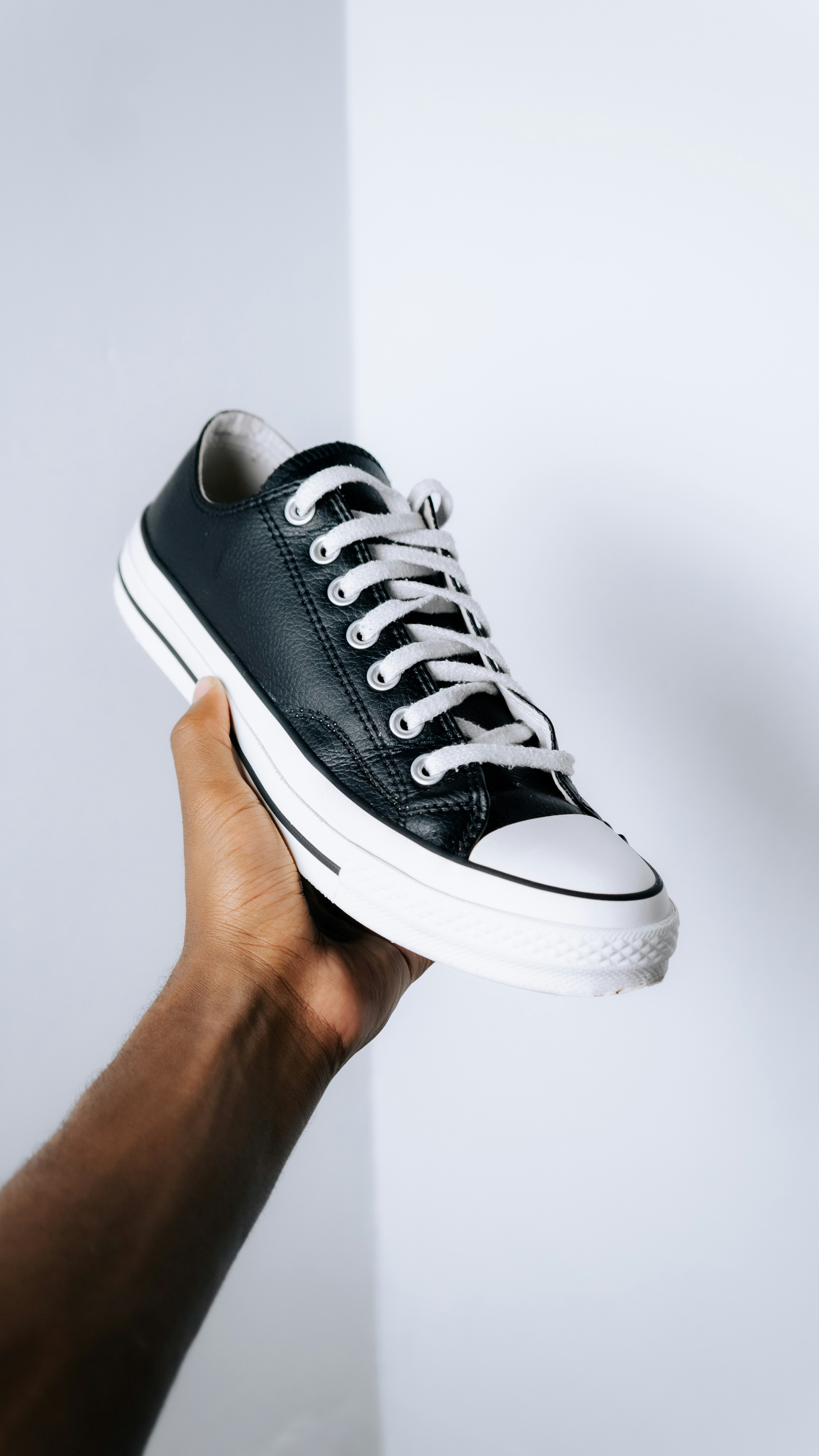 A hand holds a black converse shoe.