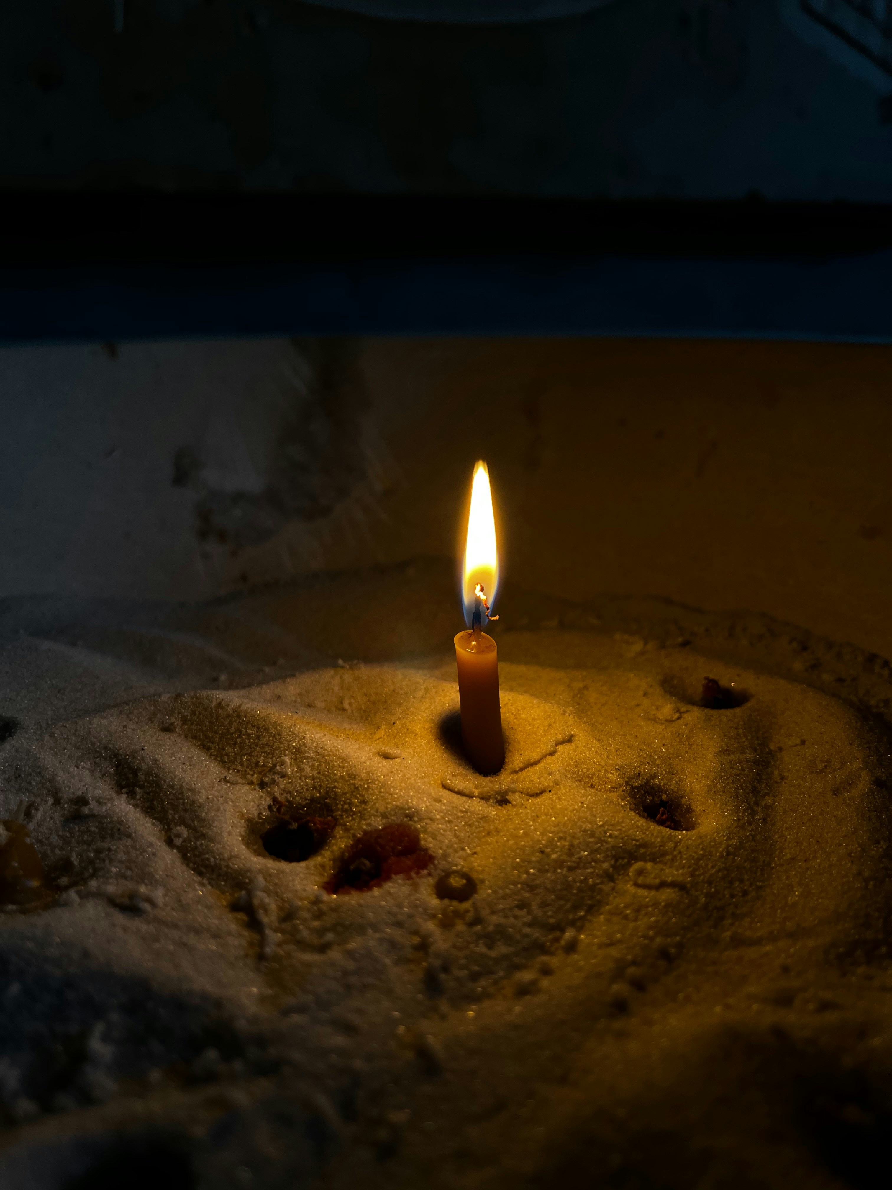 A lit candle burns brightly in the sand.