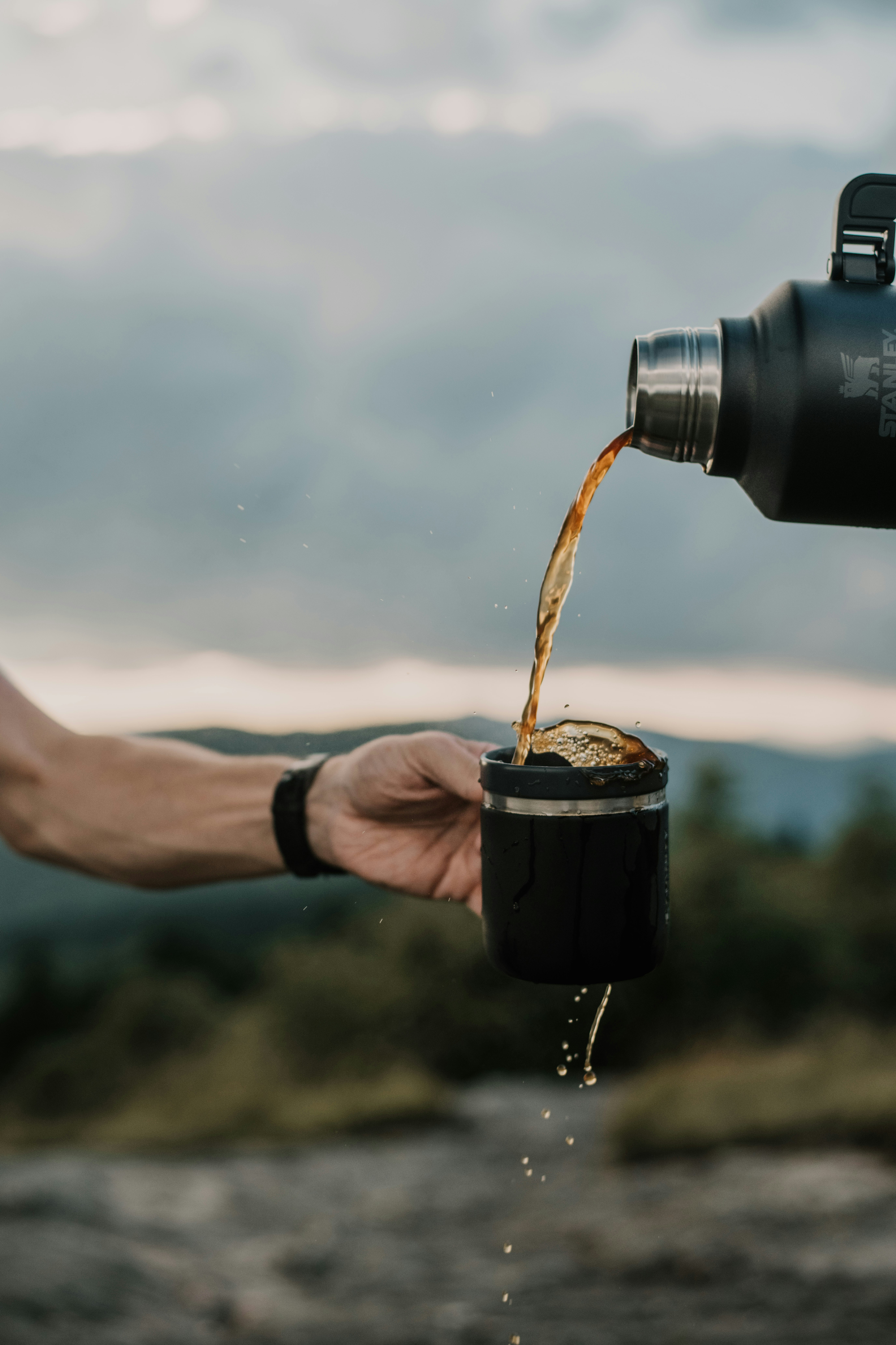 Trailside Pour: Amber Flow Into a Mug Beneath a Misty Horizon