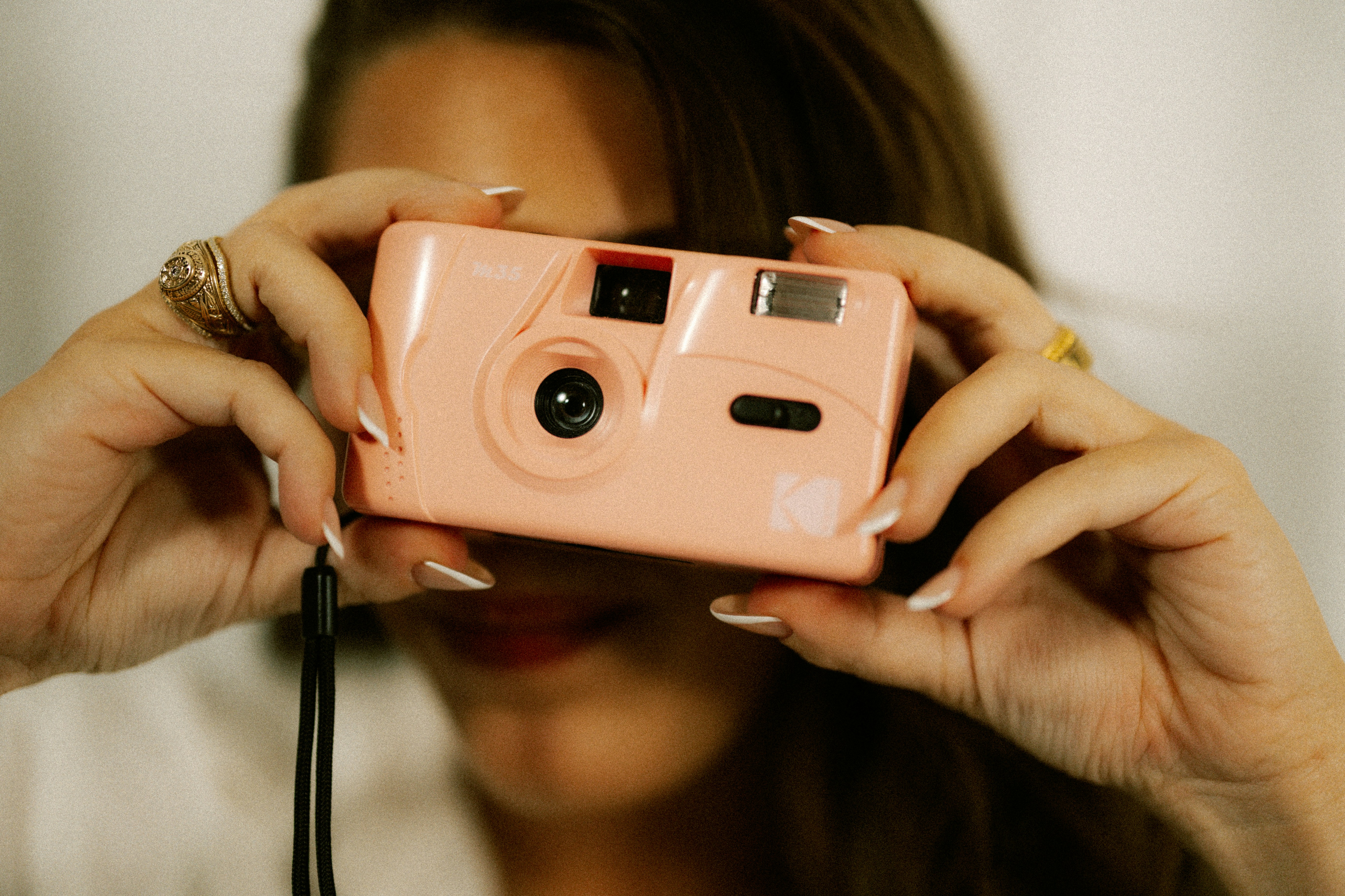 A person holds a vintage Kodak camera, preparing to capture a moment. The soft focus highlights the camera's retro design and the subject's playful demeanor.