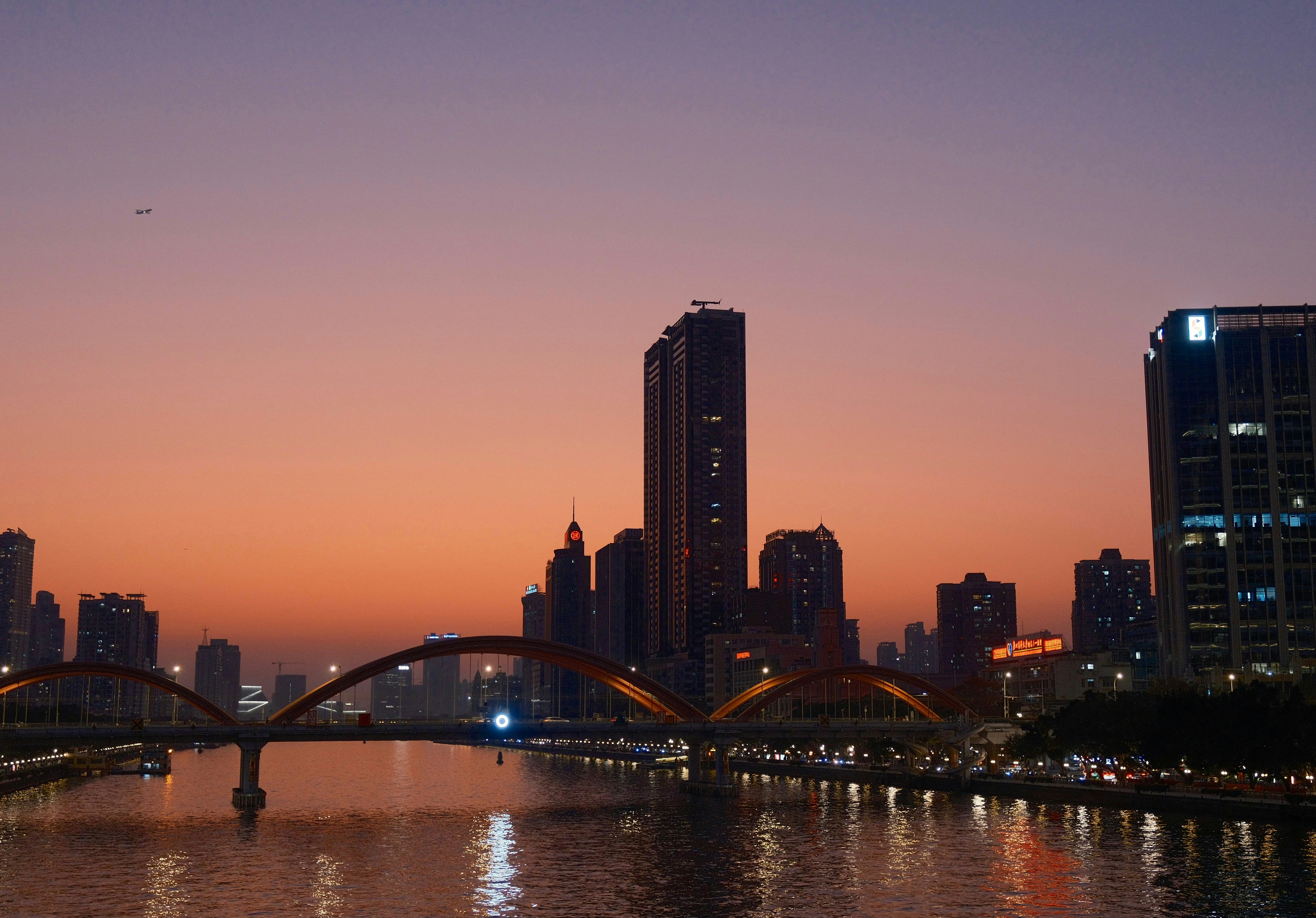 Silhouetted skyline against a gradient twilight sky, featuring a vibrant bridge arching over the river. The scene captures the essence of urban life at dusk.