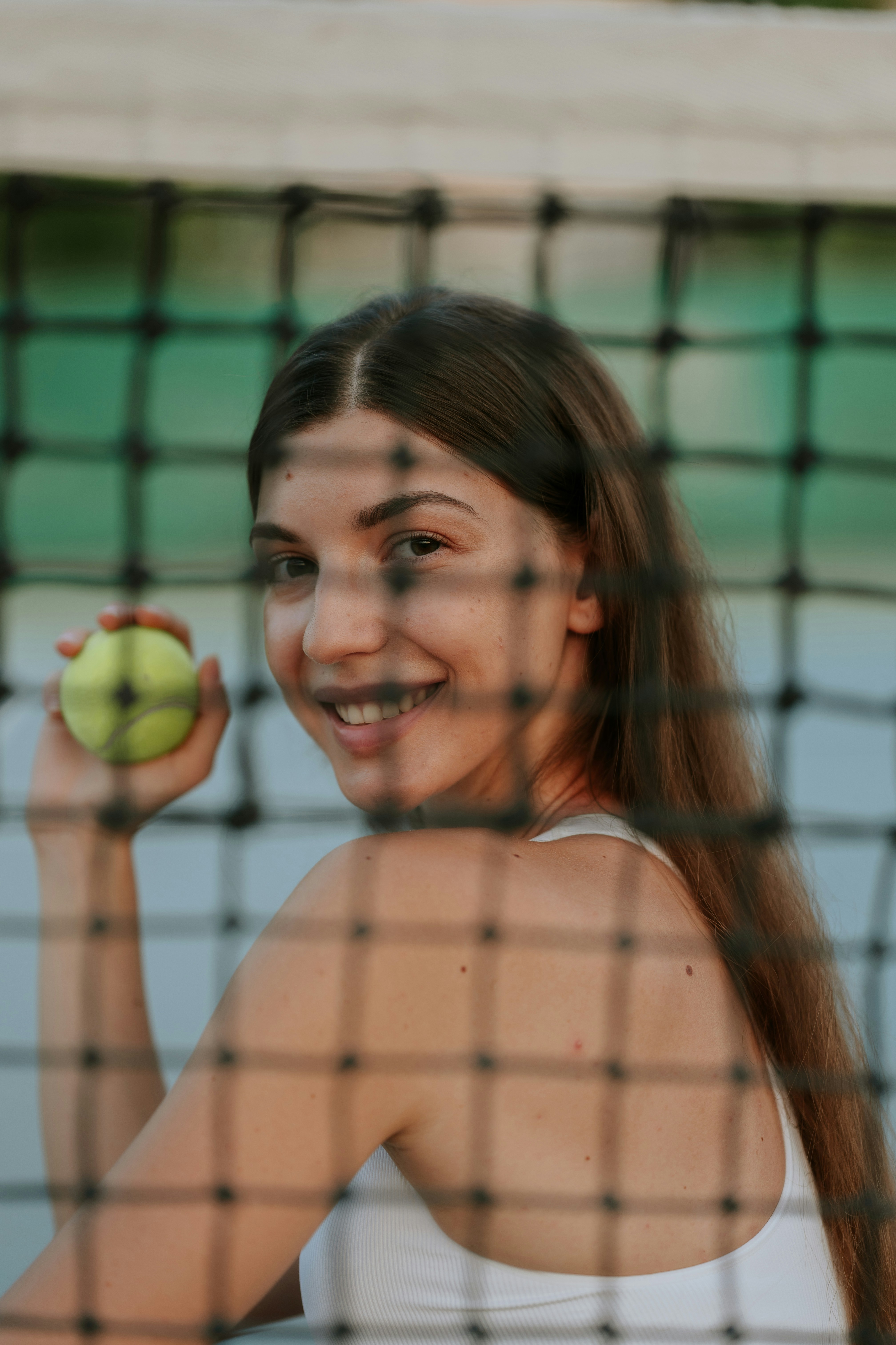Smiling woman with tennis ball behind the net.