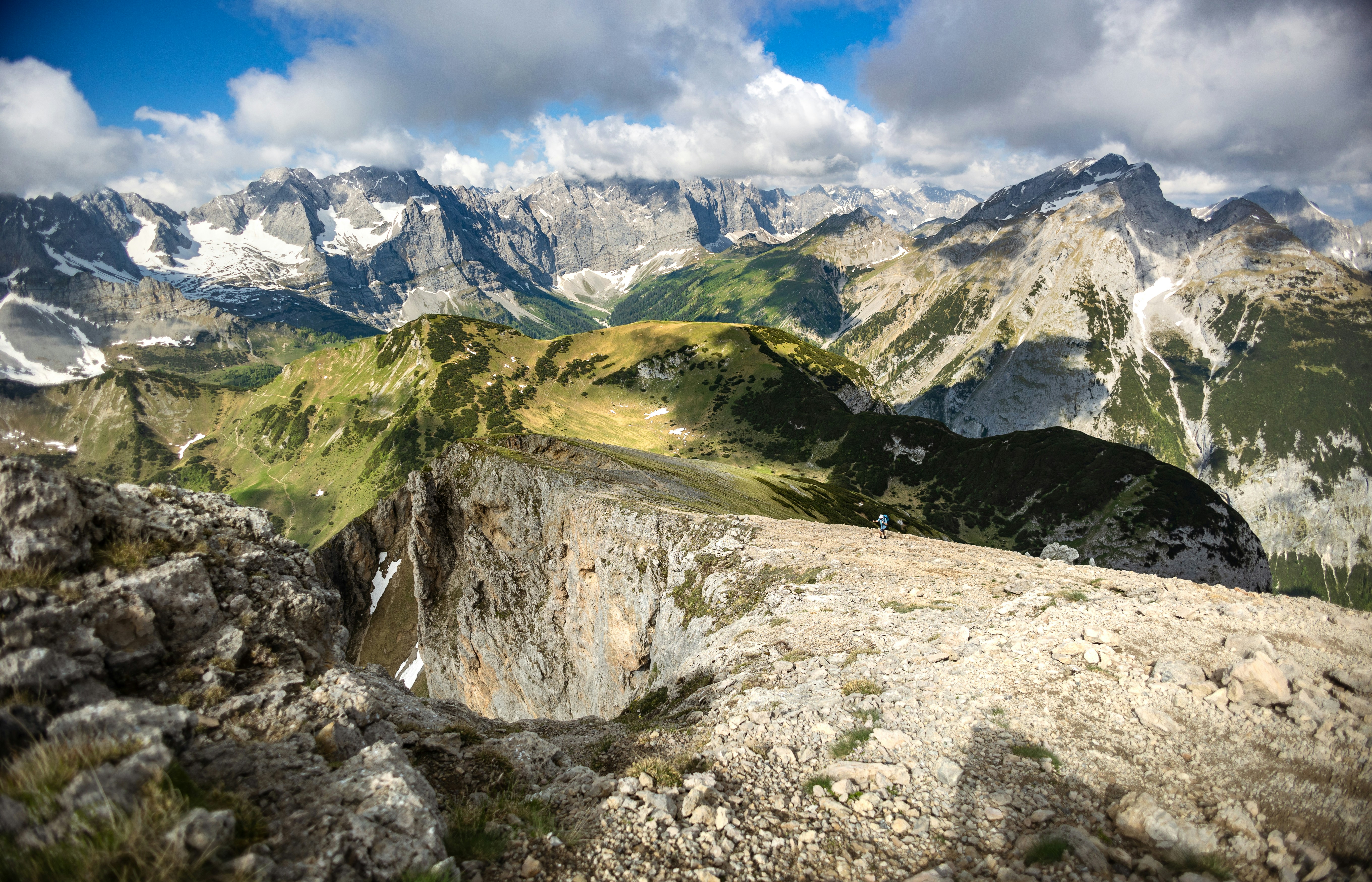Vast alpine landscape showcasing rugged mountains, lush green valleys, and dramatic cliffs under a dynamic sky.