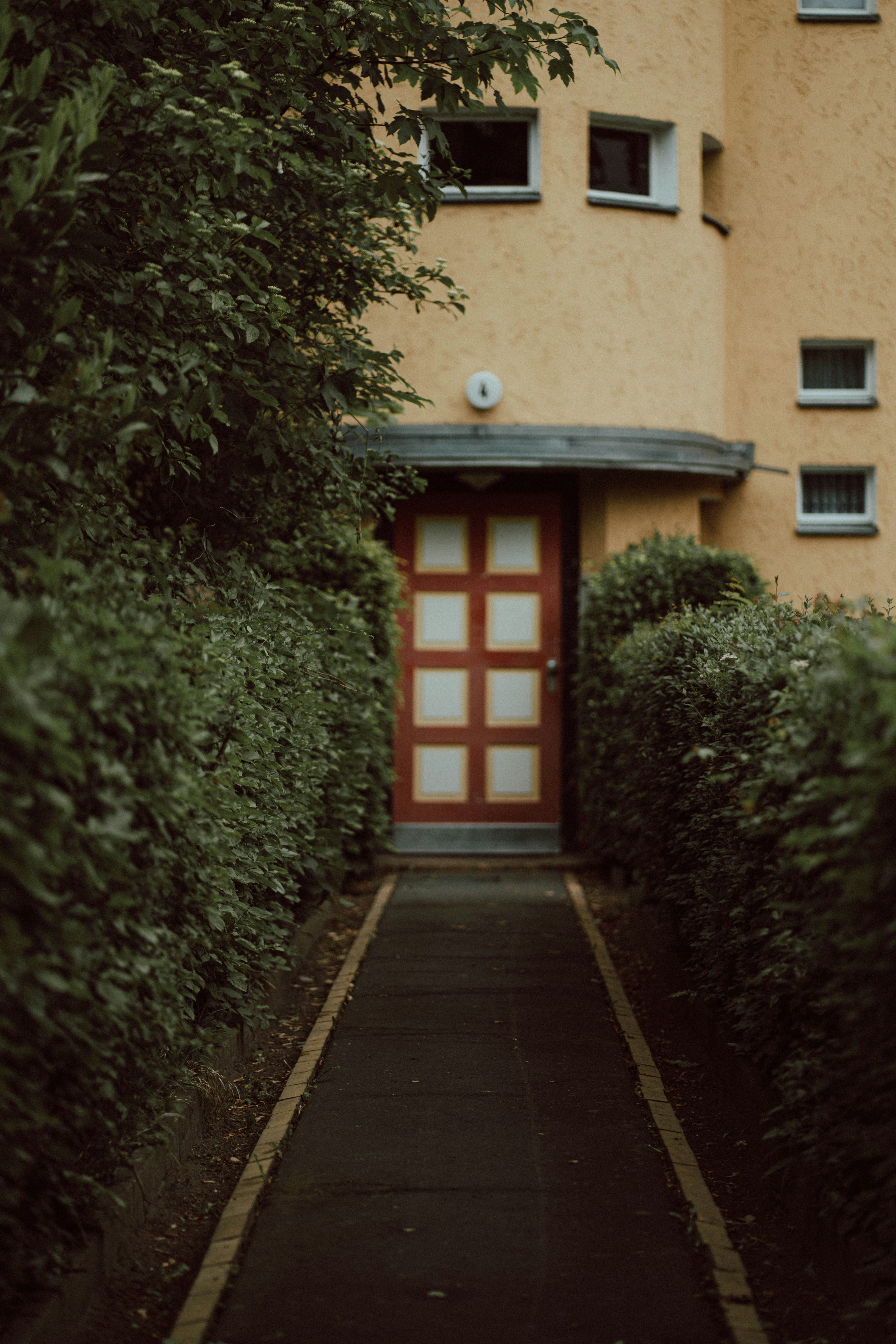 A red door beckons on a path through hedges.