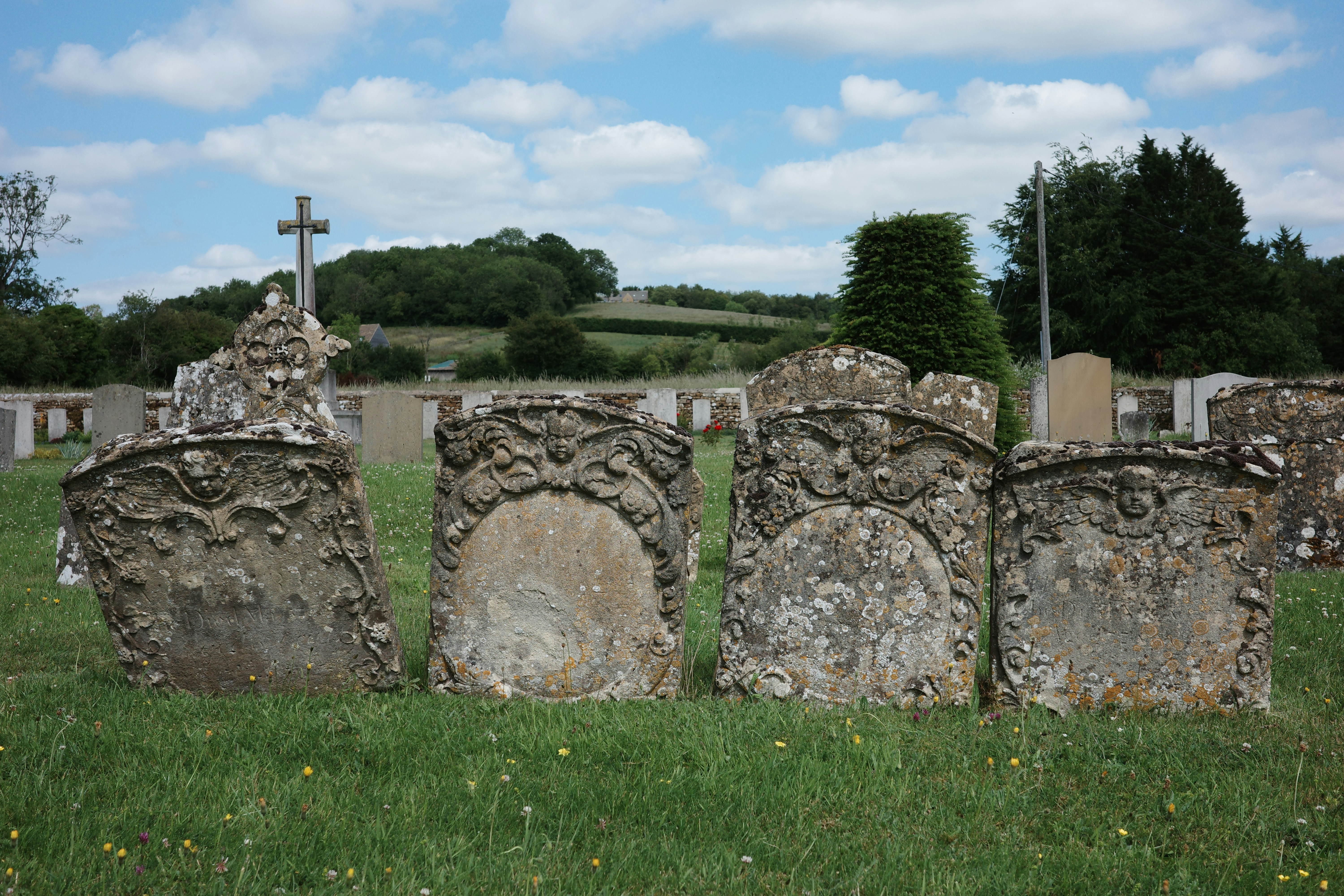 Old tombstones stand in a grassy, sunny graveyard. photo – Free Cross ...