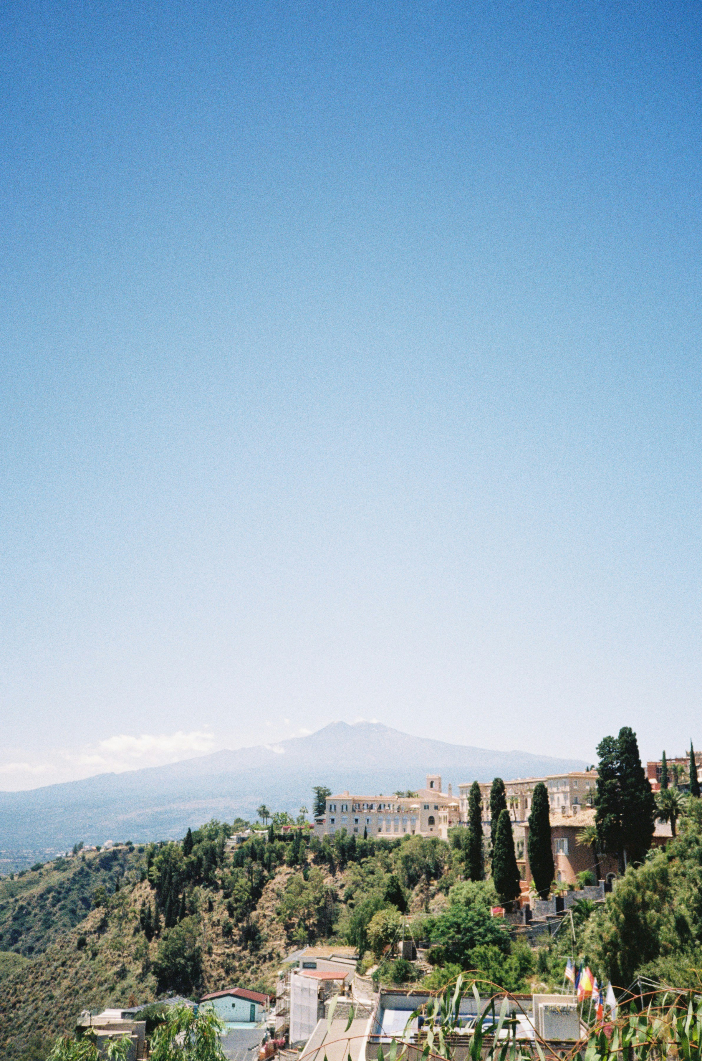 Buildings and trees with a mountain under a clear sky.
