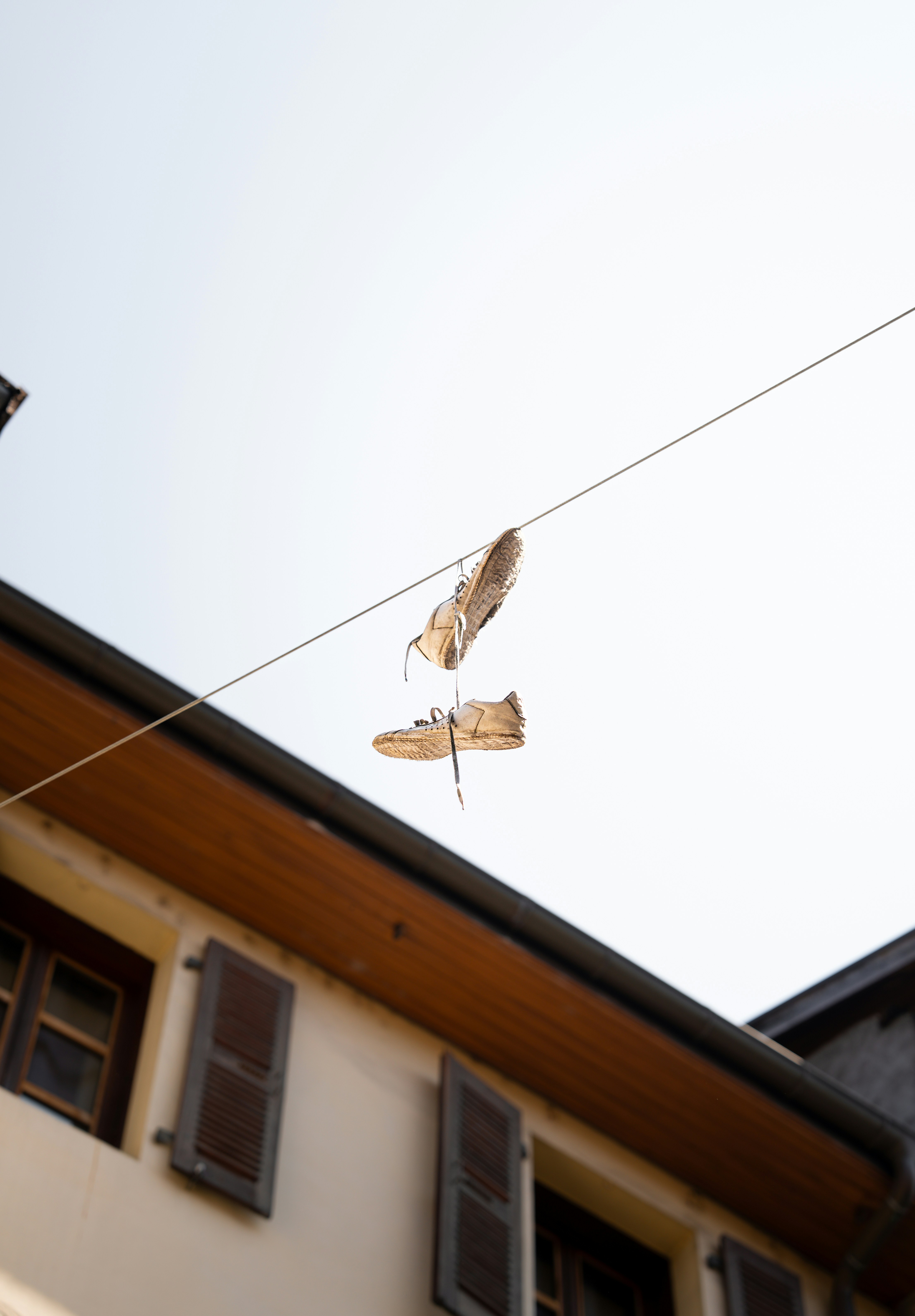 Two pairs of shoes hanging on a clothesline against a clear sky, adding a playful touch to the urban landscape.
