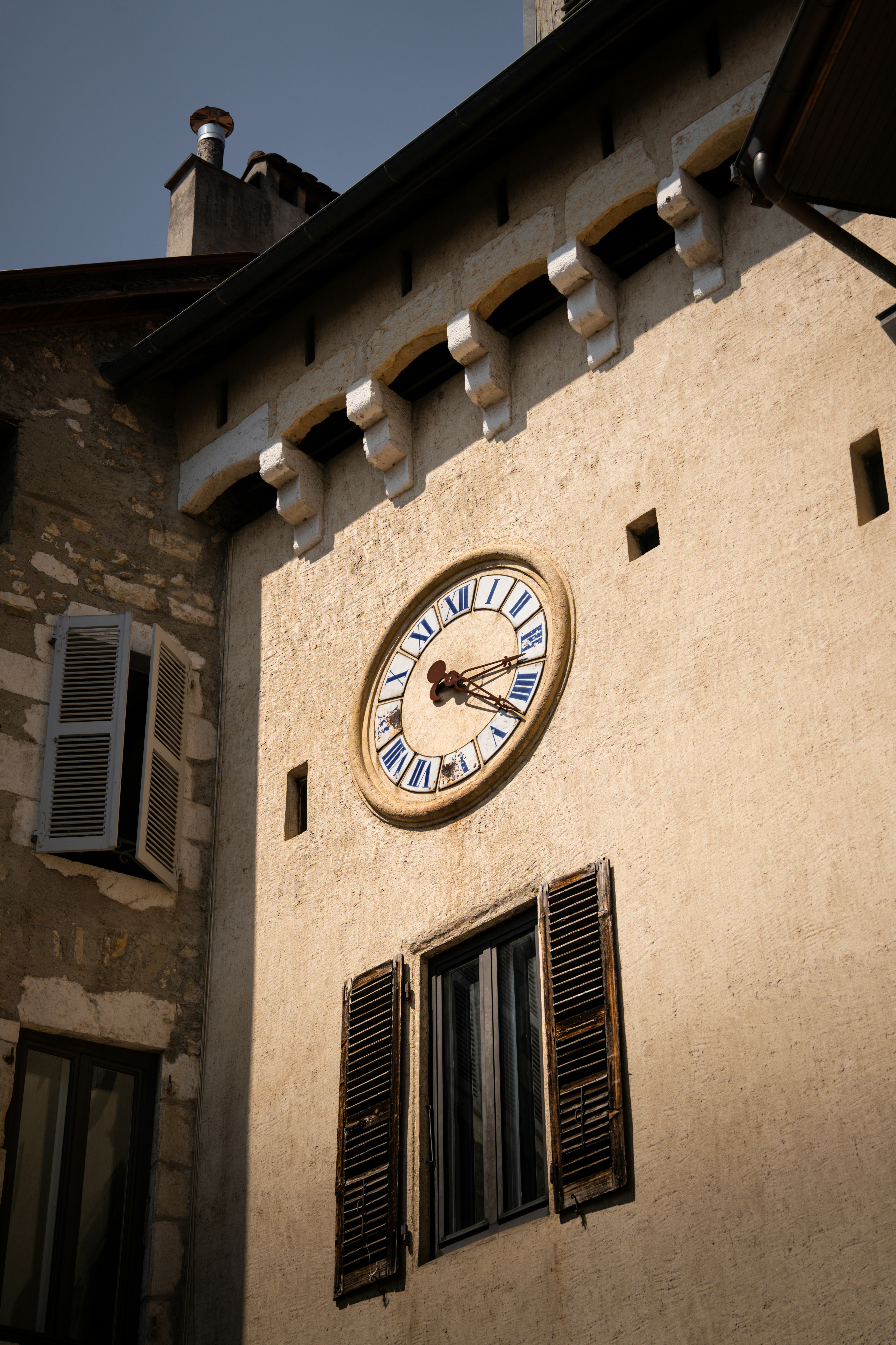 Sunlit Roman Dial on a Weathered Facade with Shuttered Windows