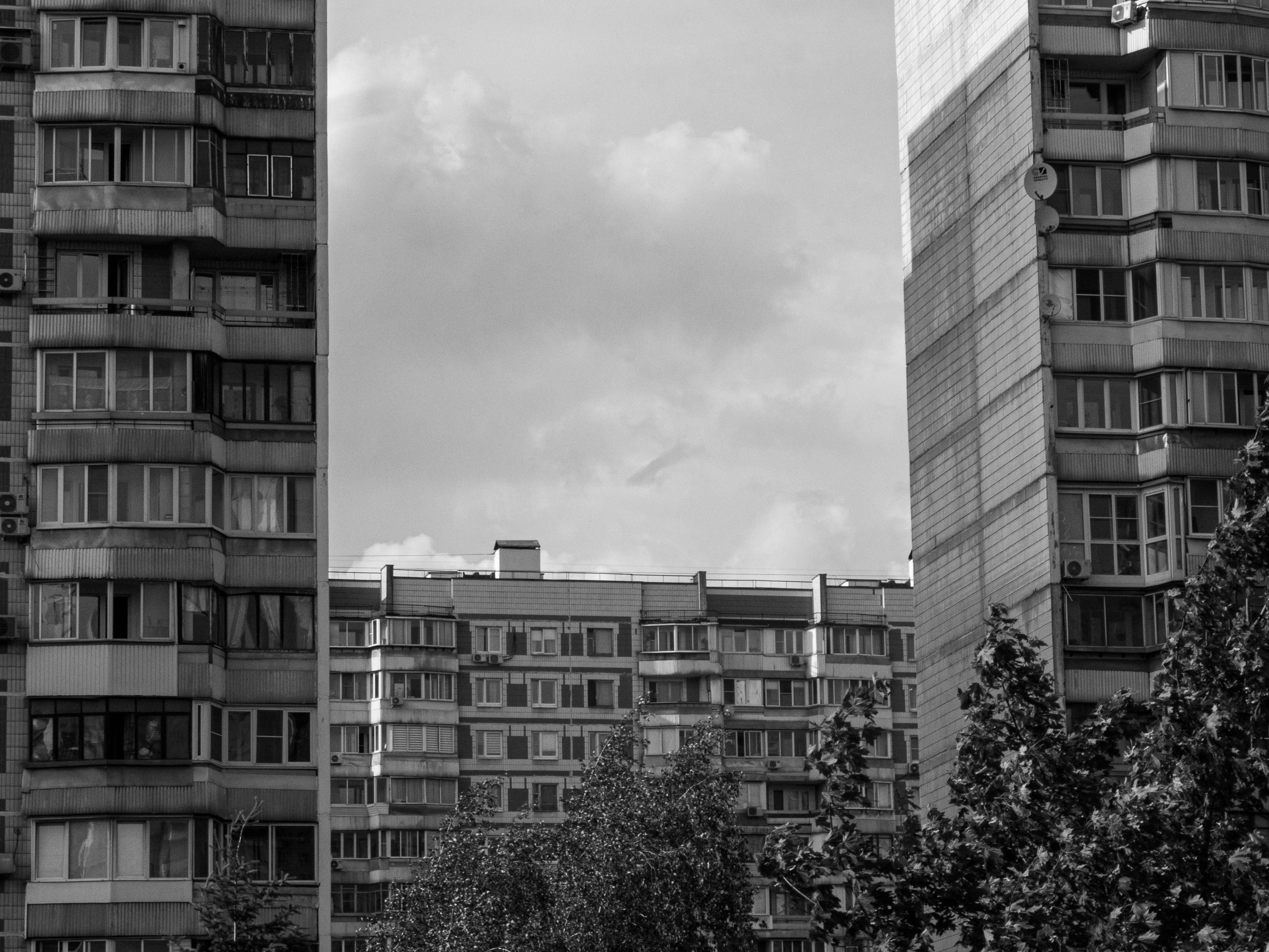 Two towering apartment buildings frame a central view of a lower structure, all captured in striking black and white. The clouds add depth to the urban landscape.