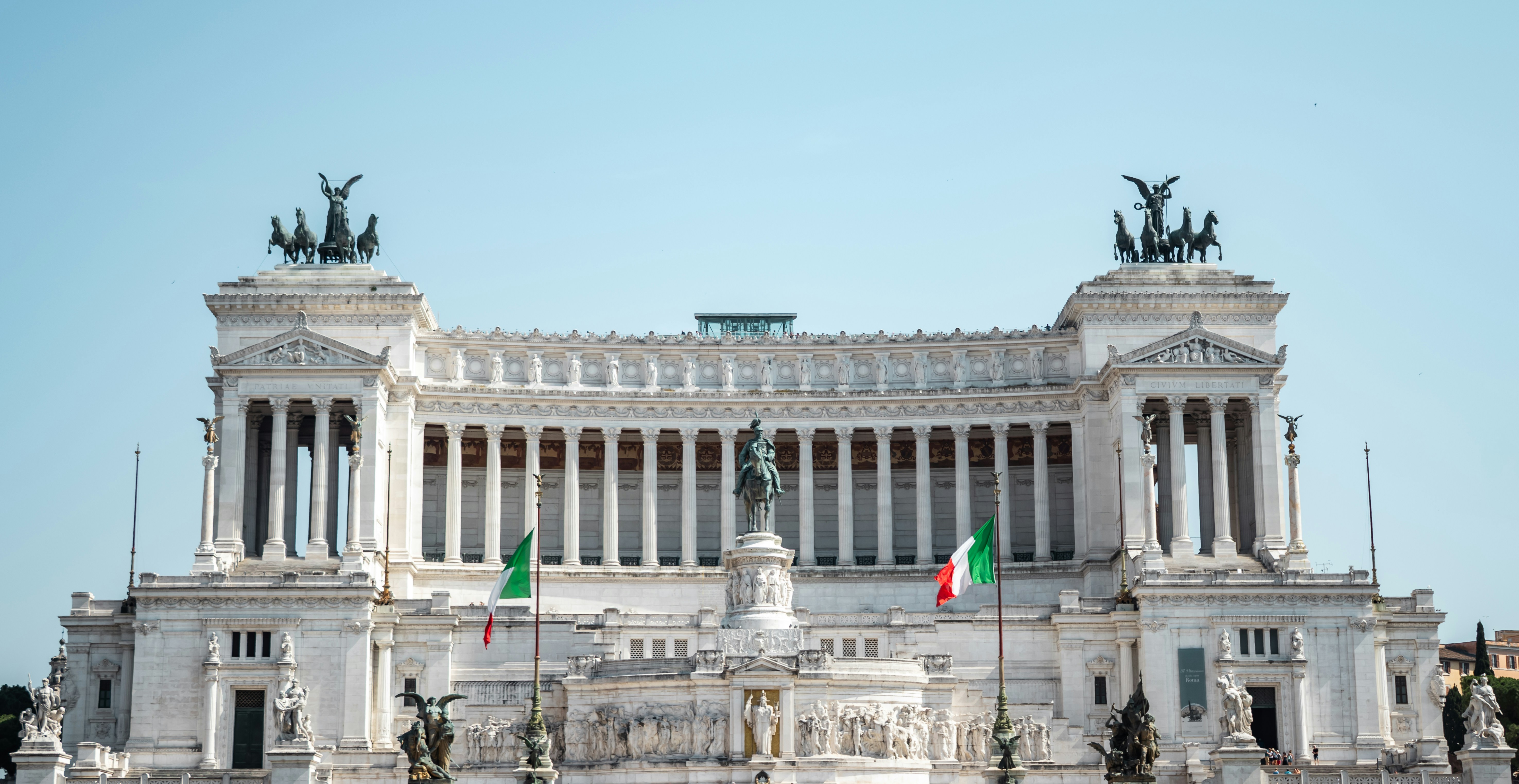 The Altare della Patria, adorned with majestic statues and Italian flags, stands proudly under a clear blue sky, showcasing its architectural grandeur.