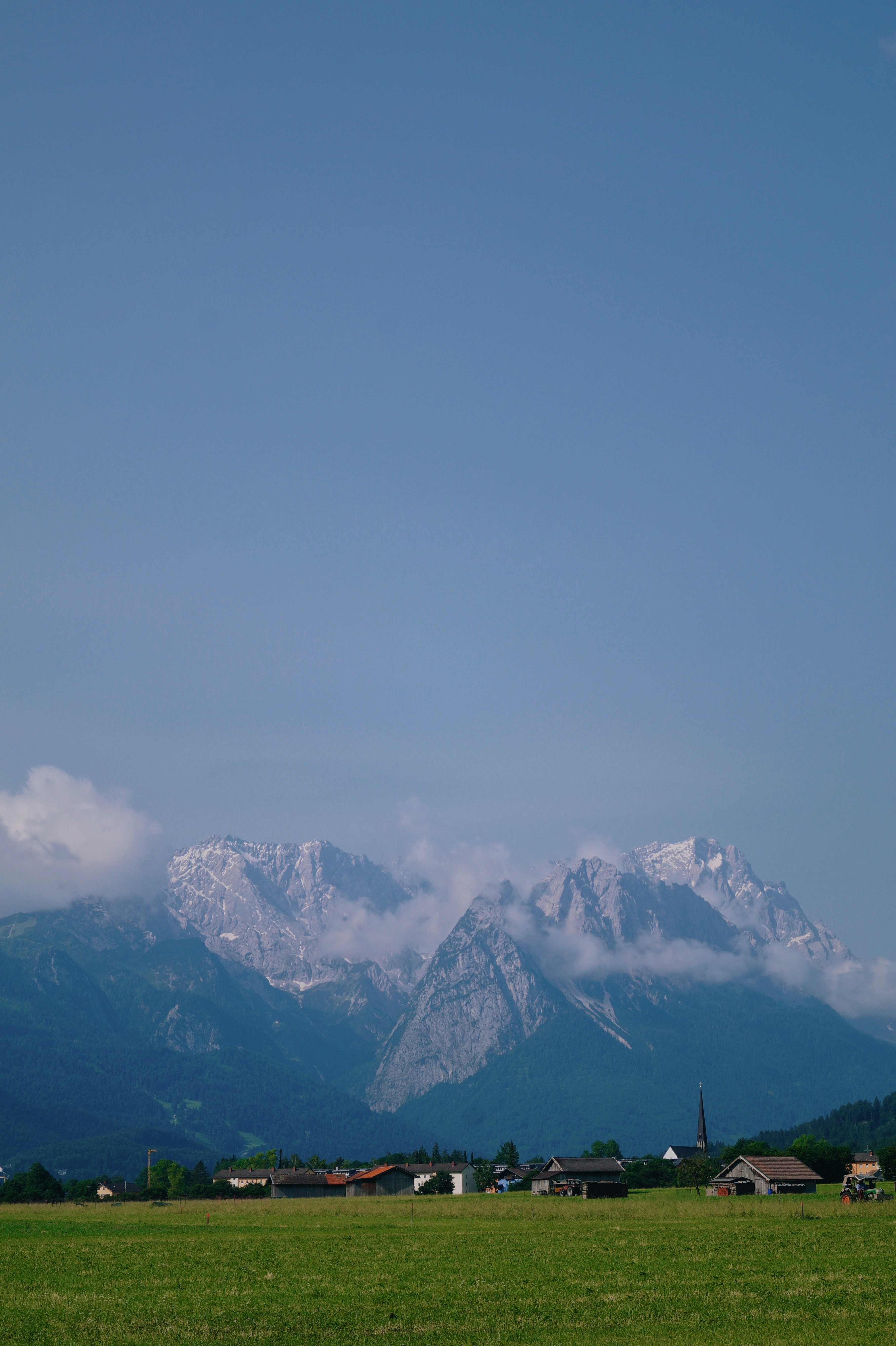Mountains rise above a village and a green field.