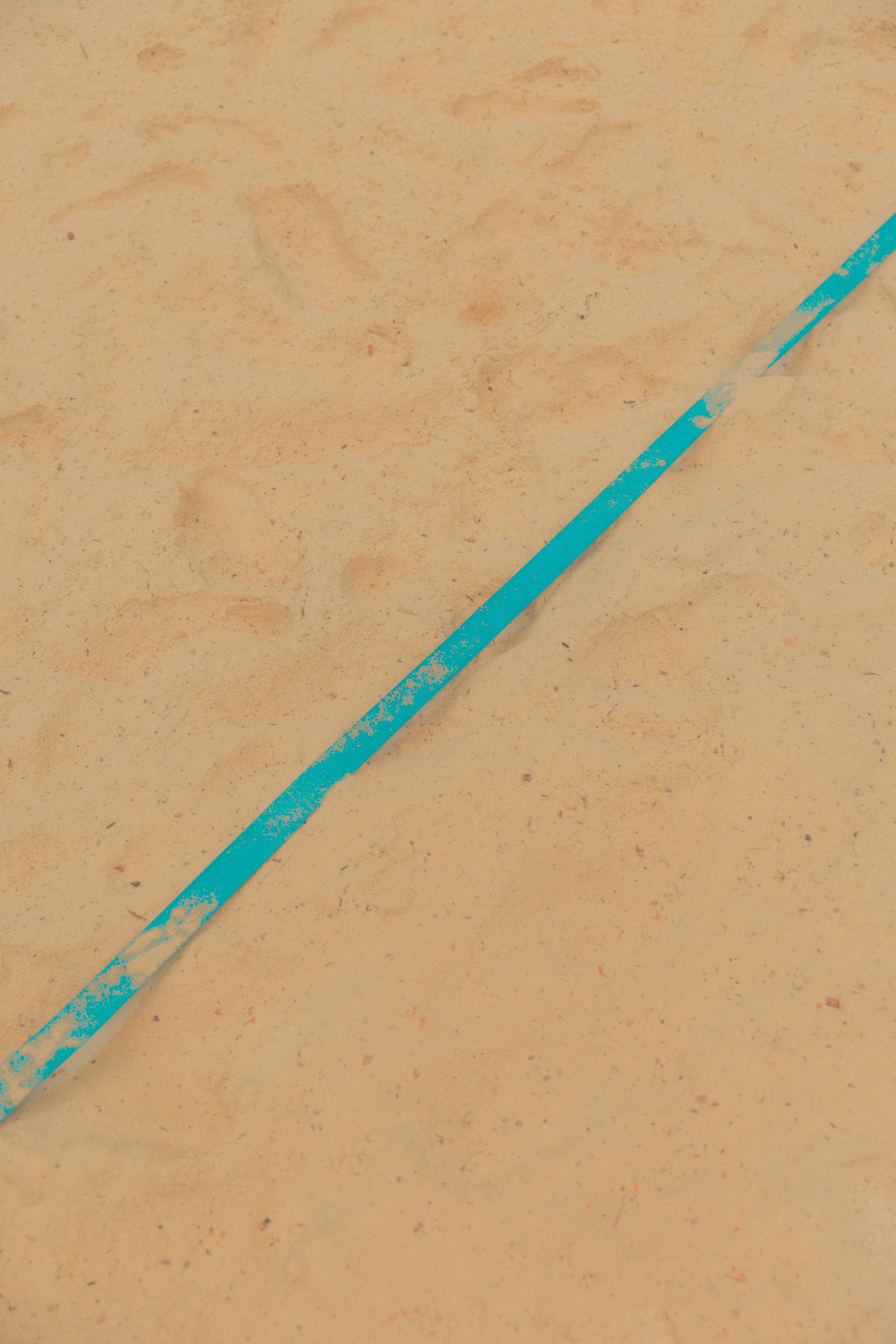 A vibrant blue line stretches across a sandy beach, contrasting with the soft beige tones of the sand. Footprints hint at recent activity nearby.