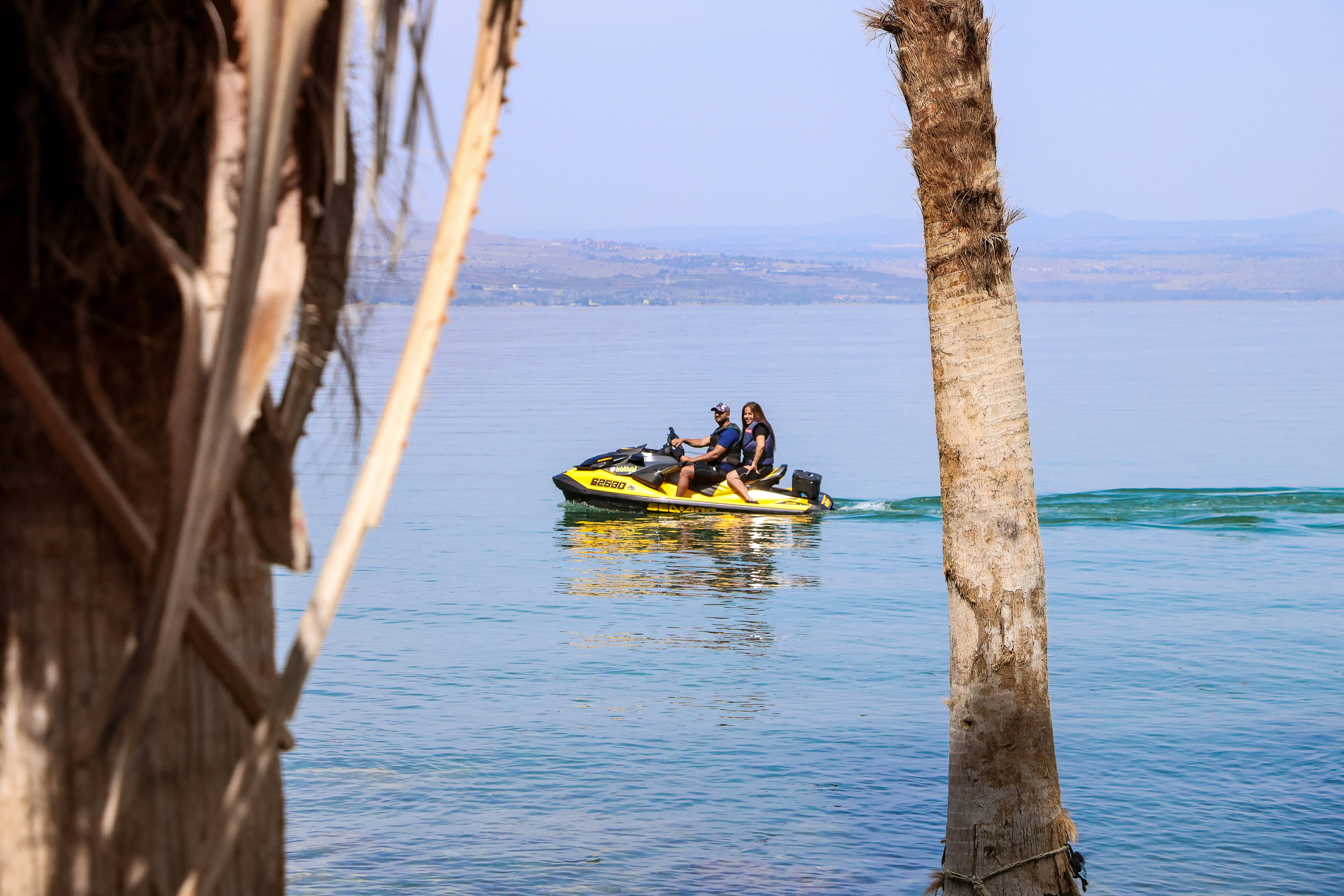 Two riders enjoying a jet ski on a tranquil lake, framed by palm trees in the foreground. 