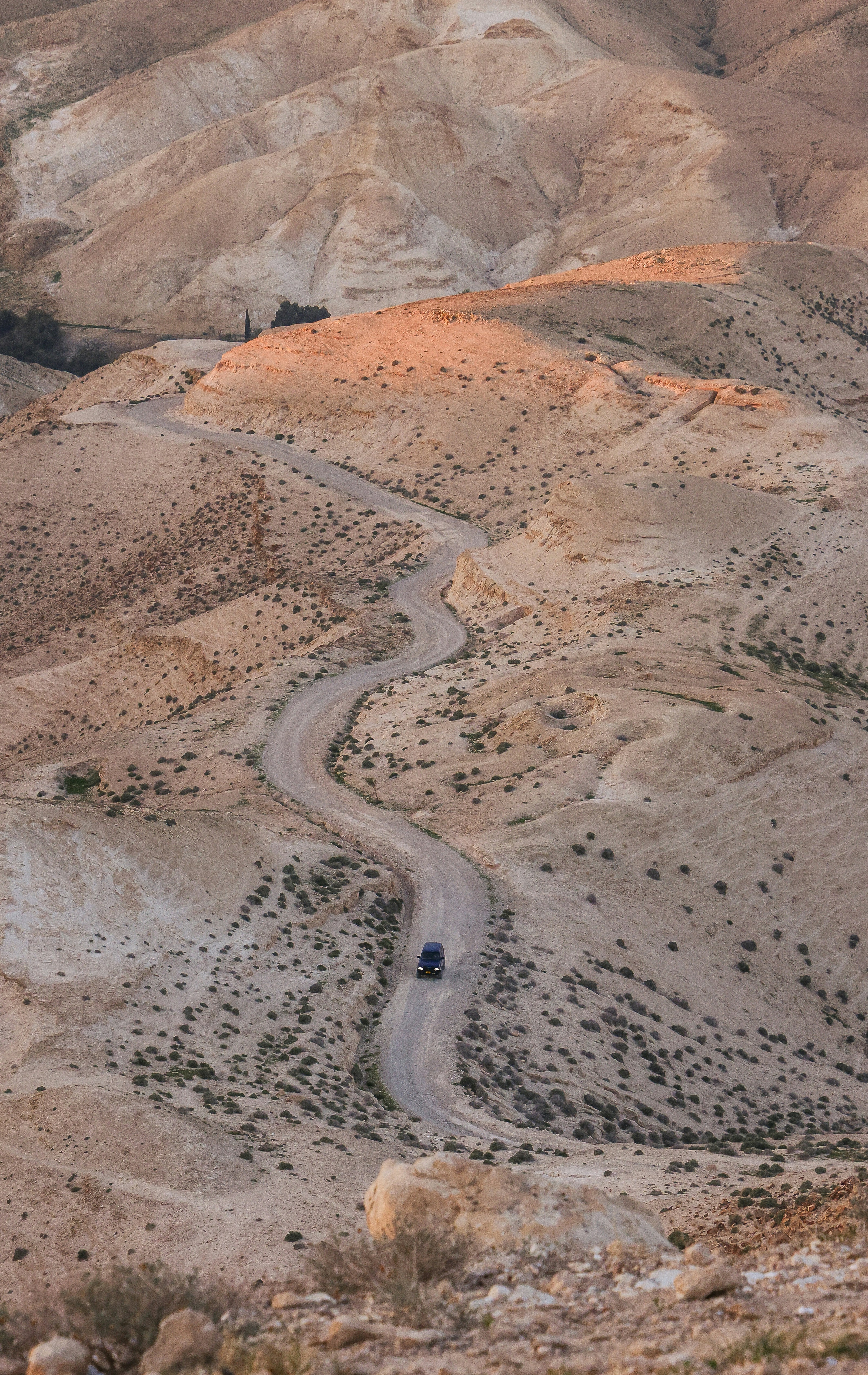 A car drives along a winding road in the desert.
