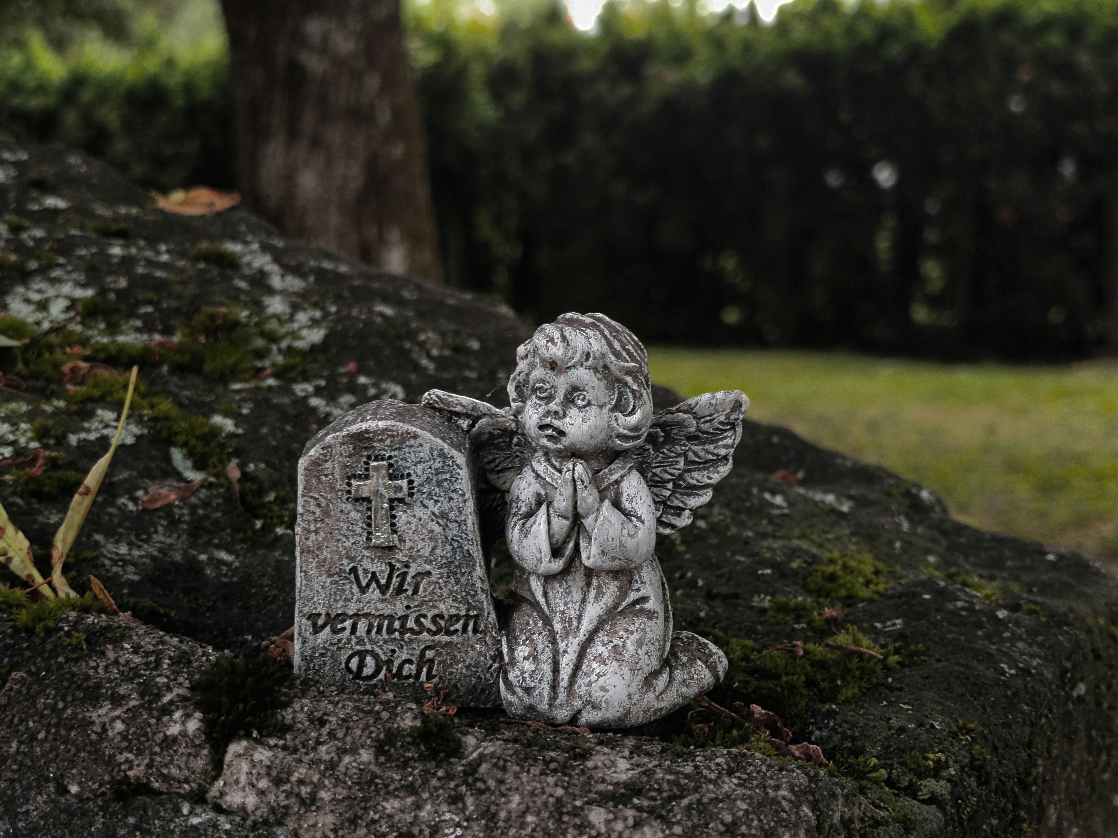 An angel statue kneels beside a tombstone.