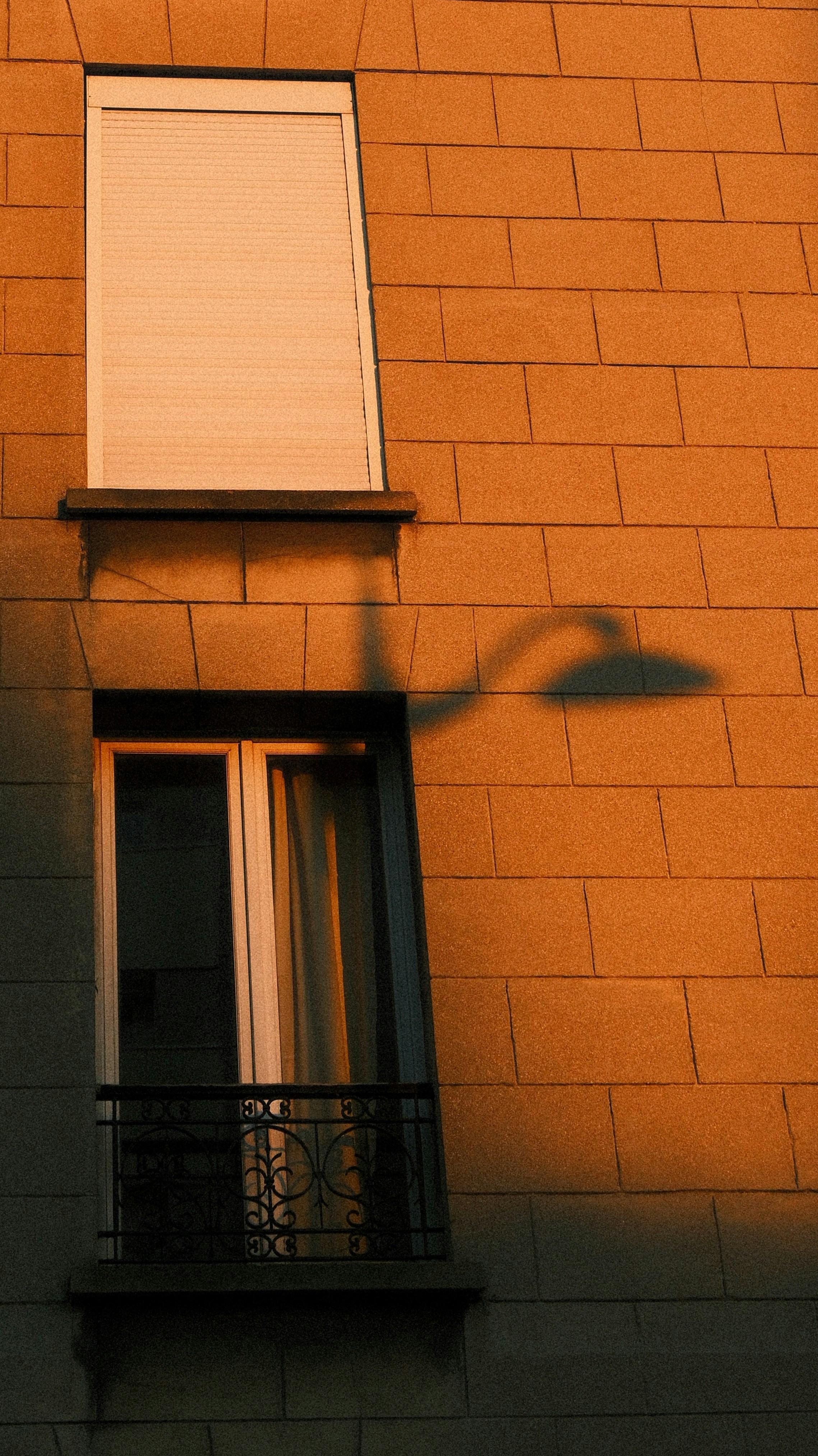 Orange Hour Shadow: A Streetlamp Cast Across a Quiet Facade