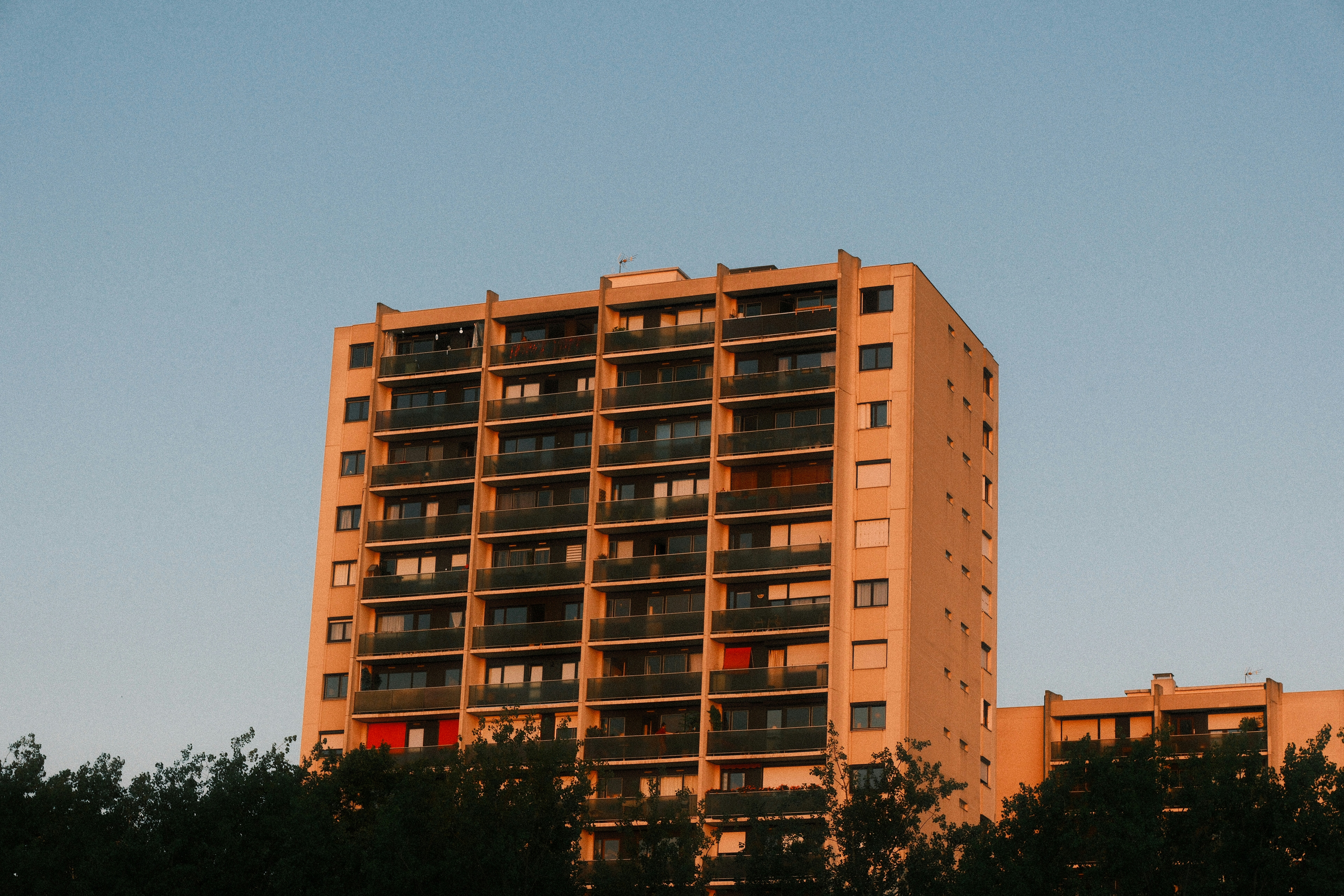colorful apartment building facing the sun during a sunset | A tall building stands against a clear blue sky.