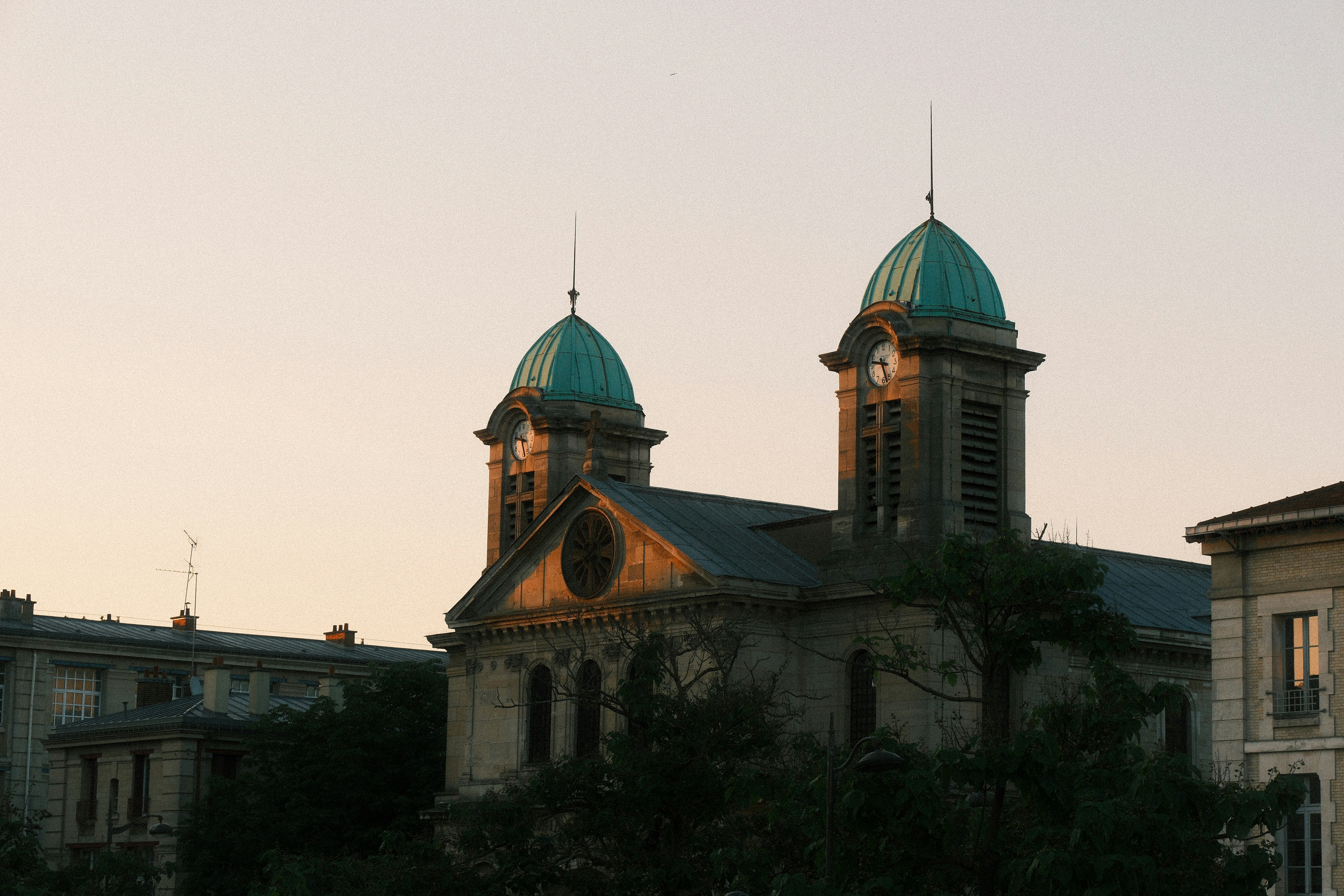Historic building with twin turquoise domes illuminated by the soft glow of sunset. The structure showcases intricate architectural details amidst a serene evening backdrop.