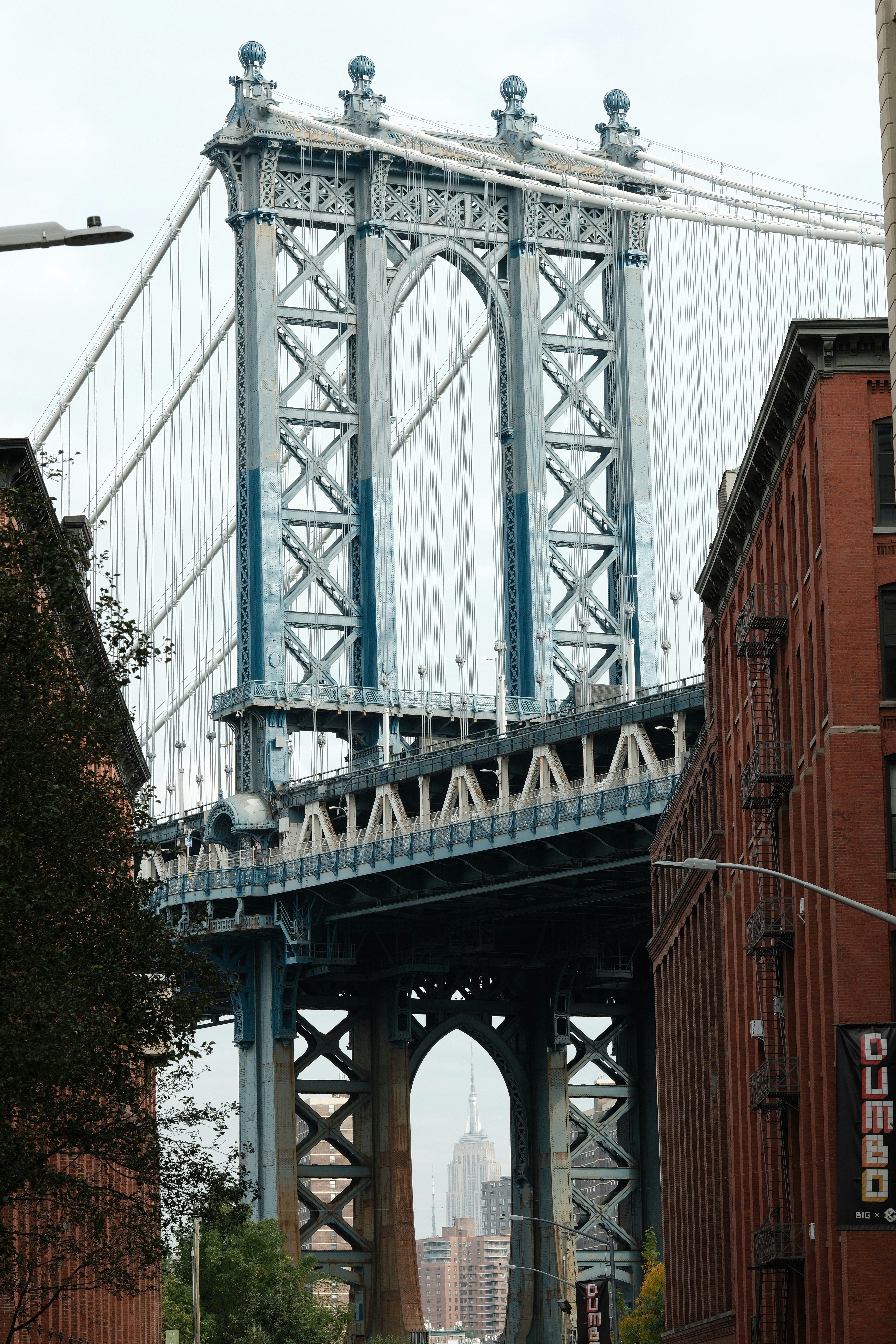 The Manhattan Bridge frames the Empire State Building, creating a striking urban composition. Vibrant architecture contrasts with the iconic skyline.