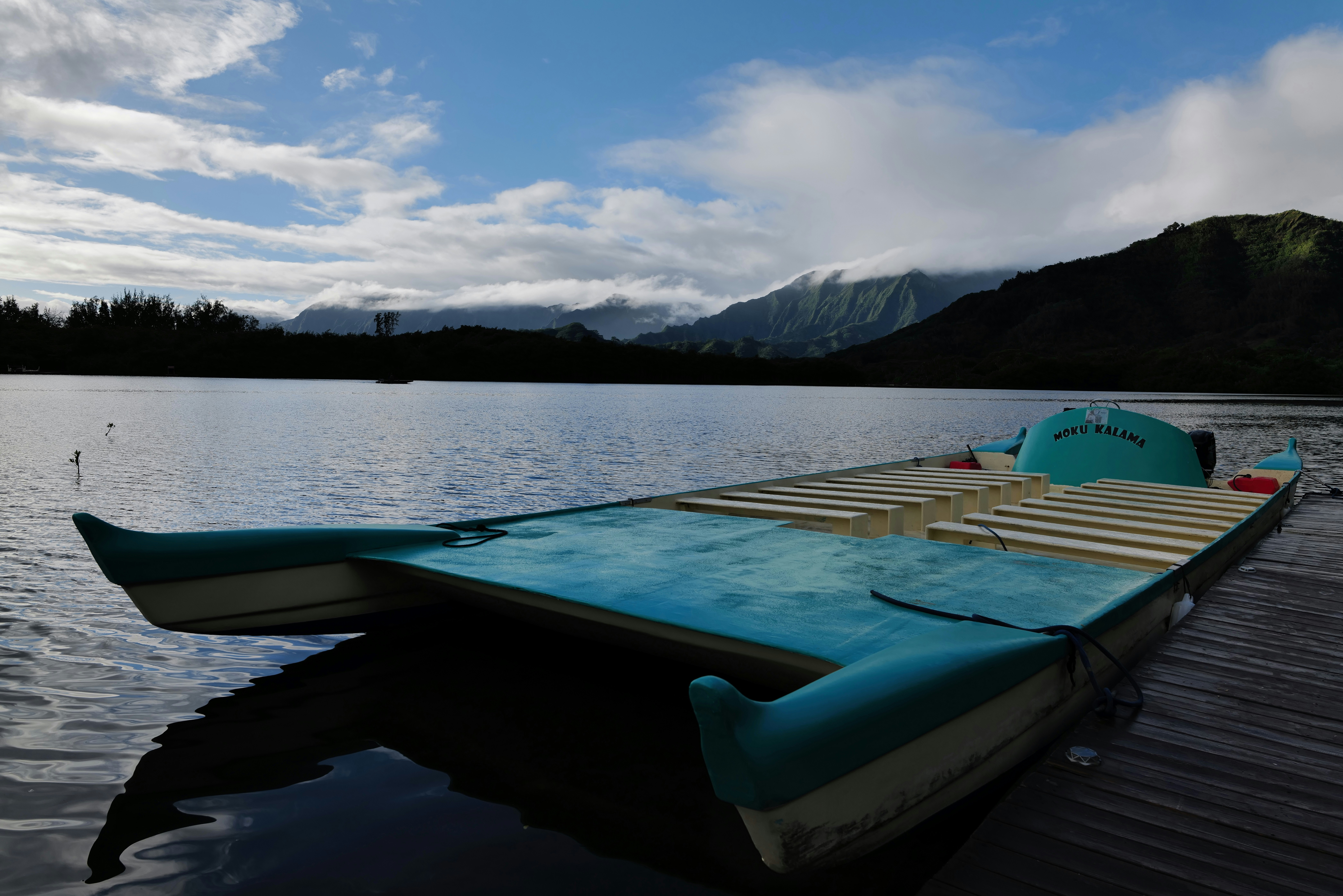 A turquoise catamaran docked on a serene lake.