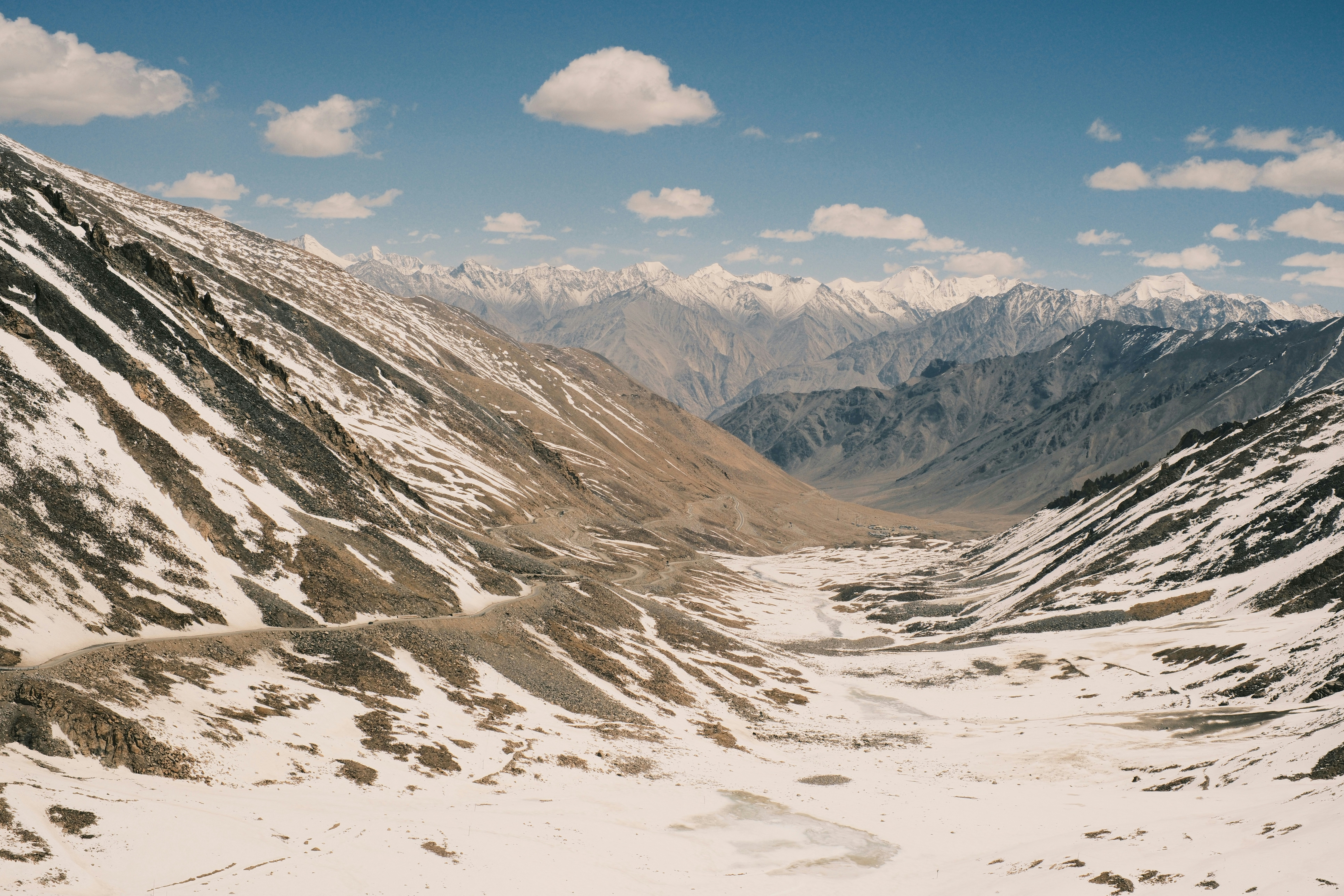 Expansive view of a snow-covered valley flanked by rugged mountains under a clear blue sky. The scene captures the stark beauty of winter landscapes.