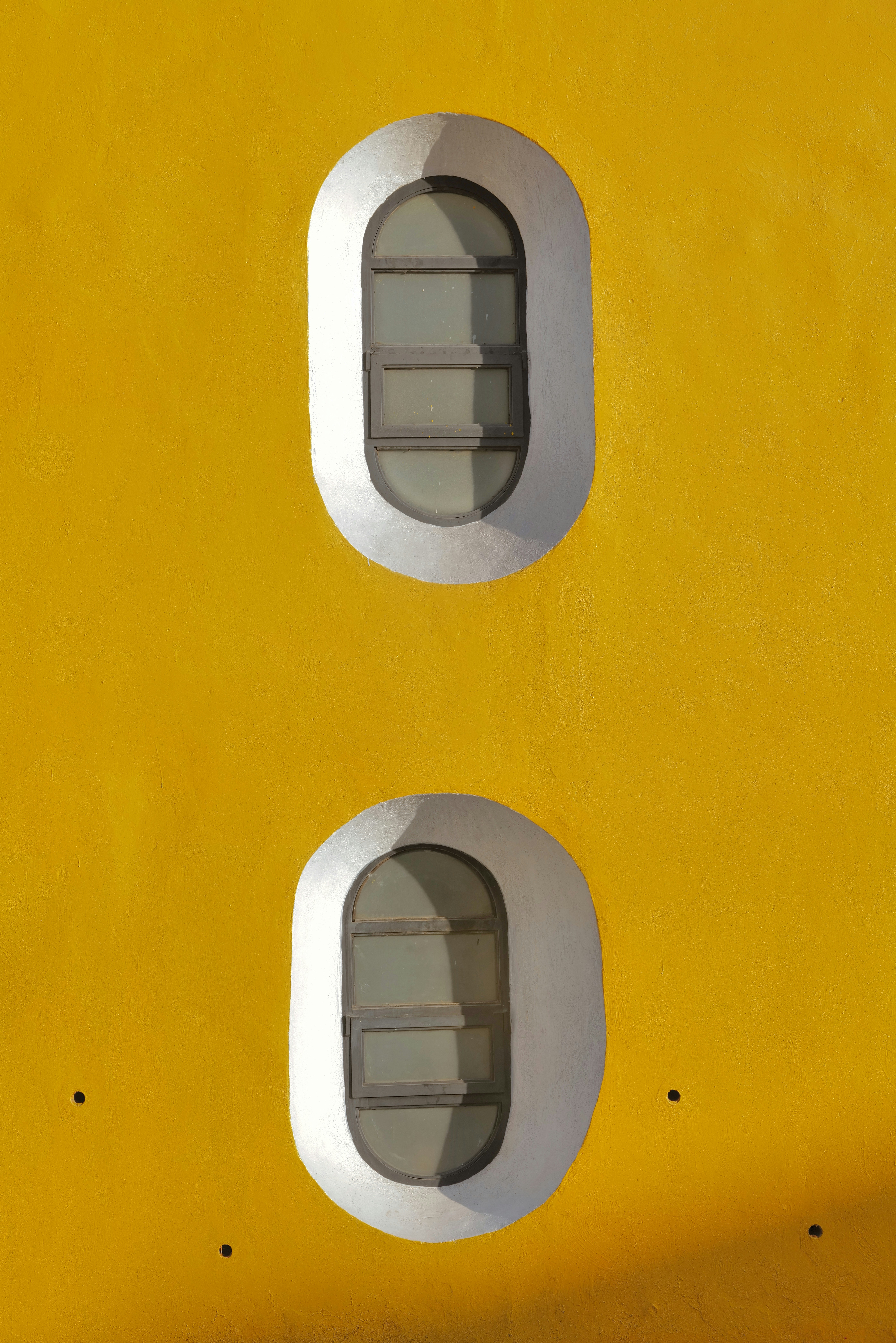Sunlit Geometry: Twin Oval Windows on a Citrus Yellow Wall