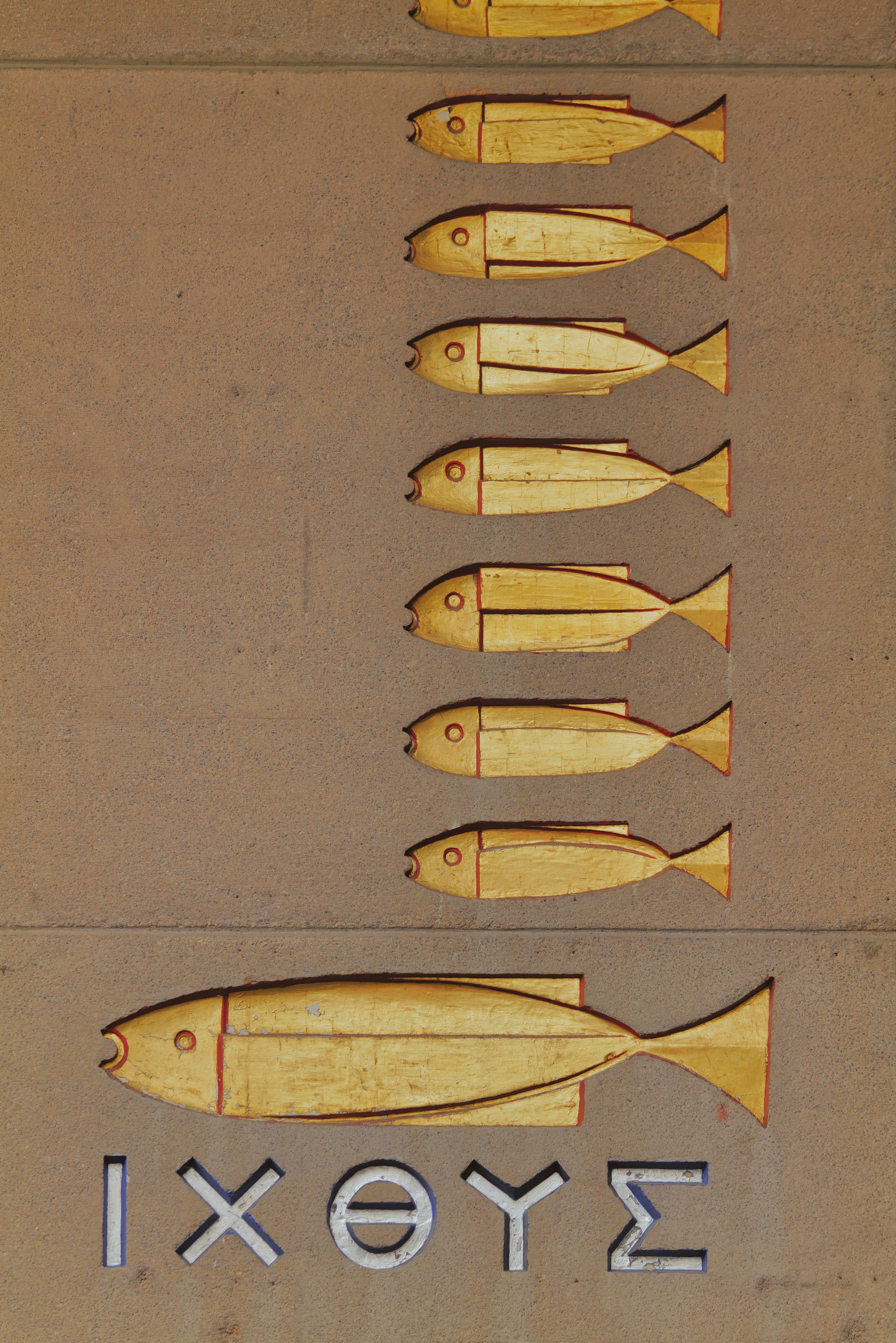 Gold-colored fish are arranged vertically above the greek word.