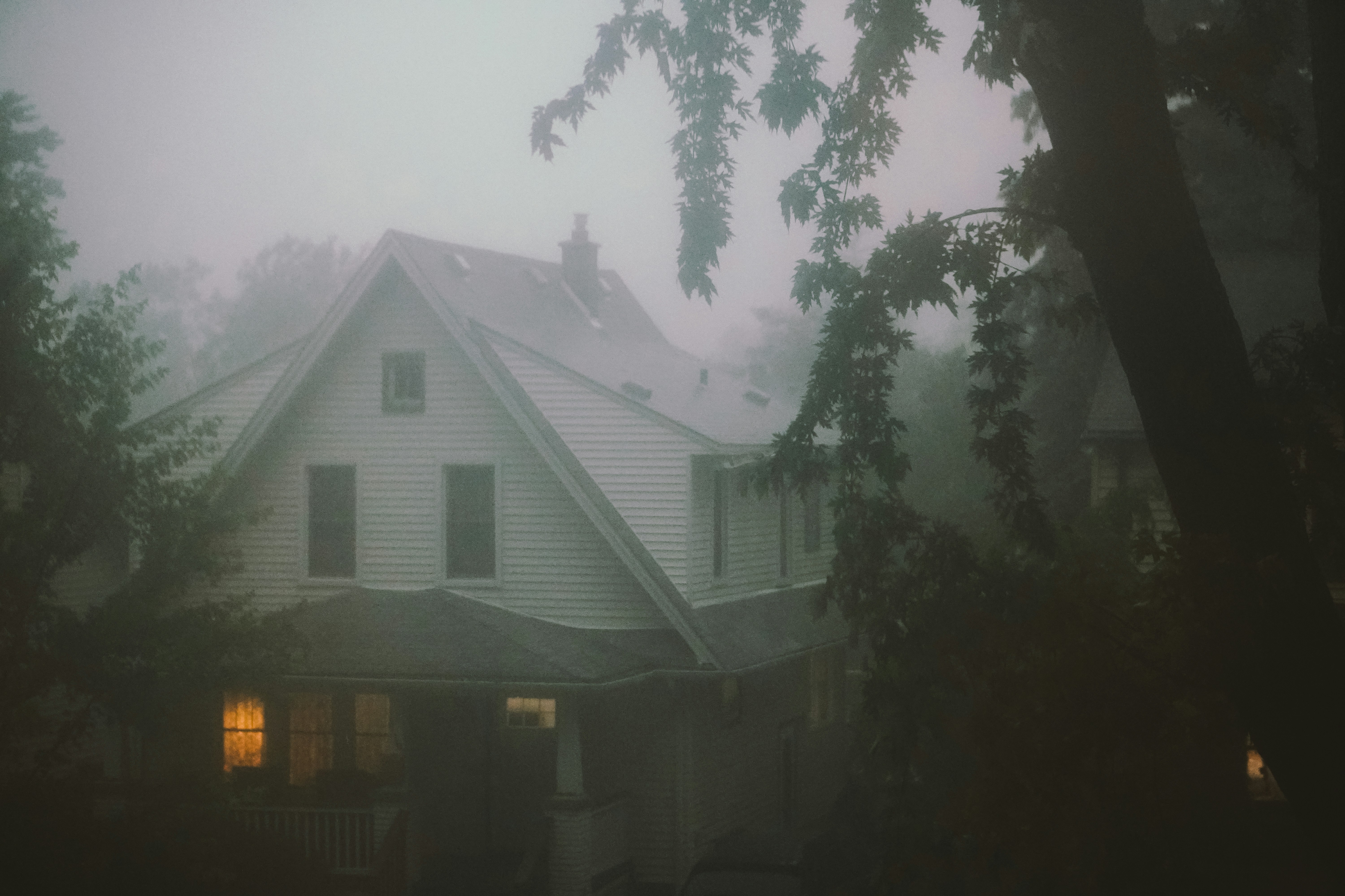 A quaint house partially obscured by thick fog, with a warm glow emanating from one window. The scene evokes a sense of mystery and tranquility.