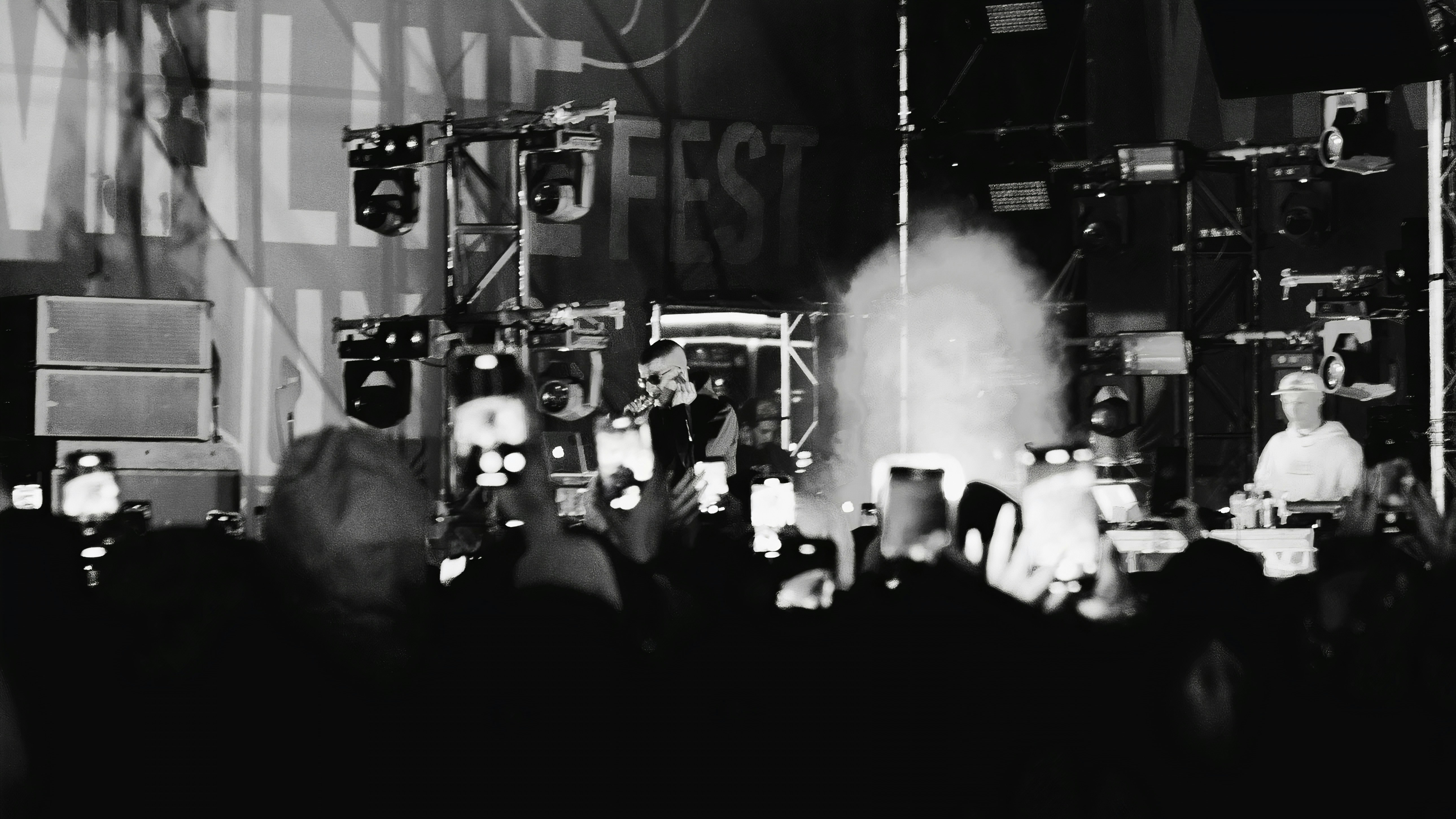 A performer captivates the audience at a music festival, surrounded by fans recording the moment on their smartphones. The scene is set against a dramatic backdrop of stage lights and sound equipment.