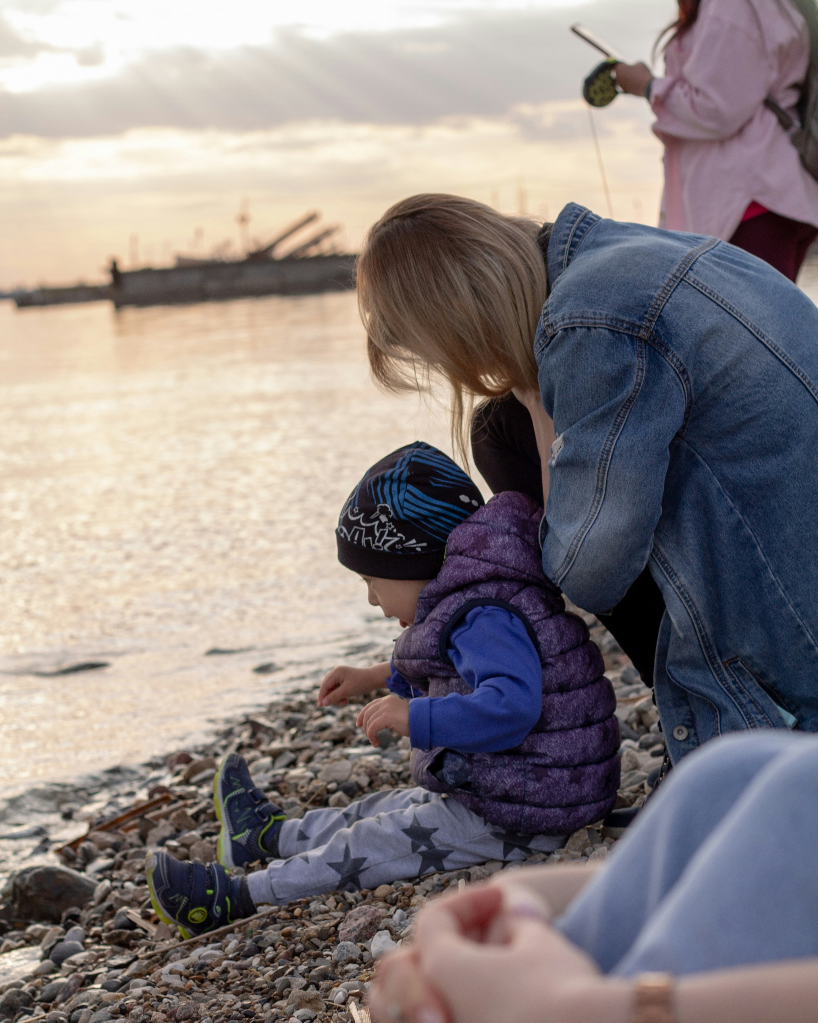 Tide-washed lesson: a mother and child share a quiet moment on the pebbled shore at sunset