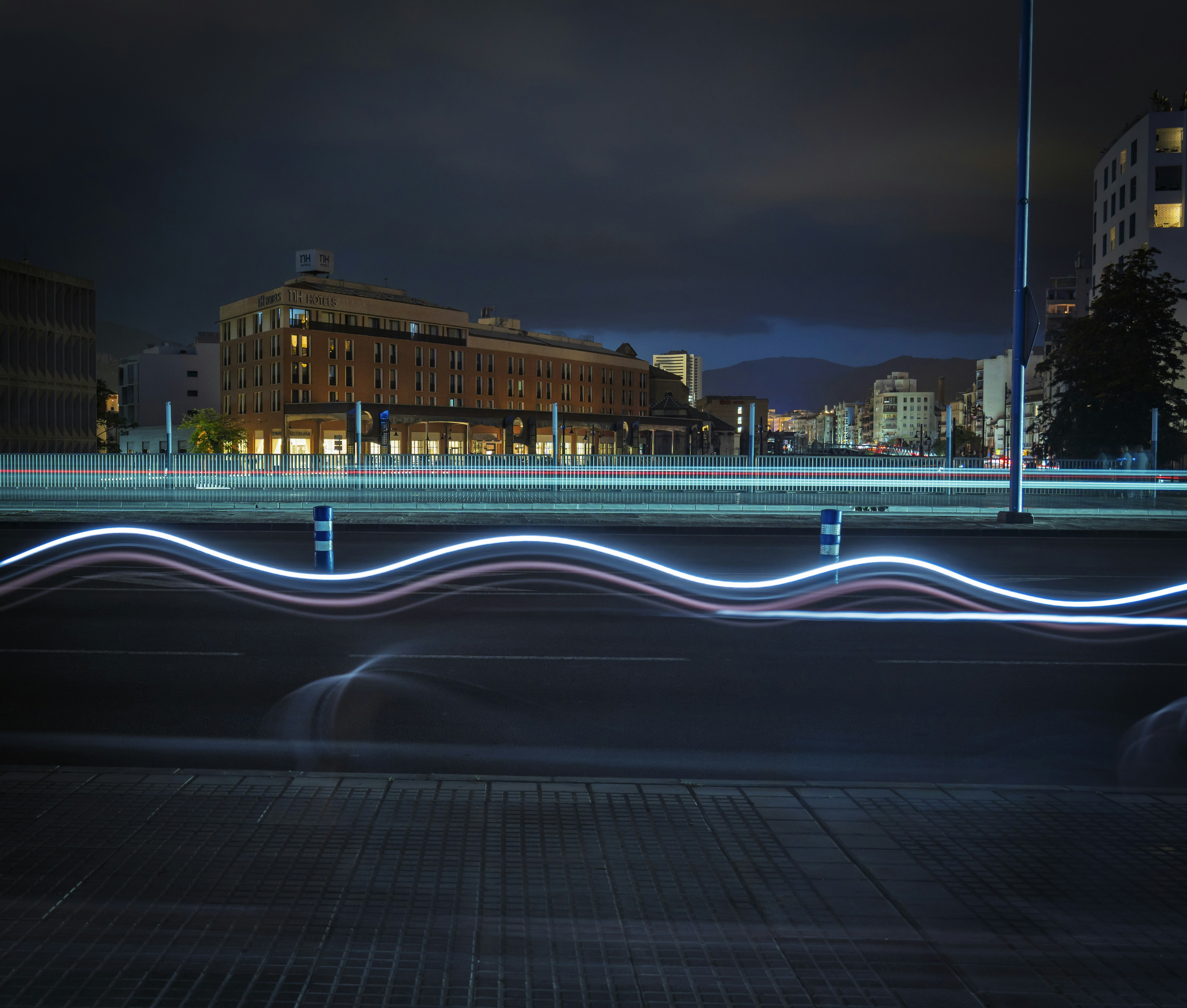 Dynamic light trails weave through a cityscape at night, showcasing the contrast between urban architecture and fleeting movement. The scene captures the essence of modern city life.