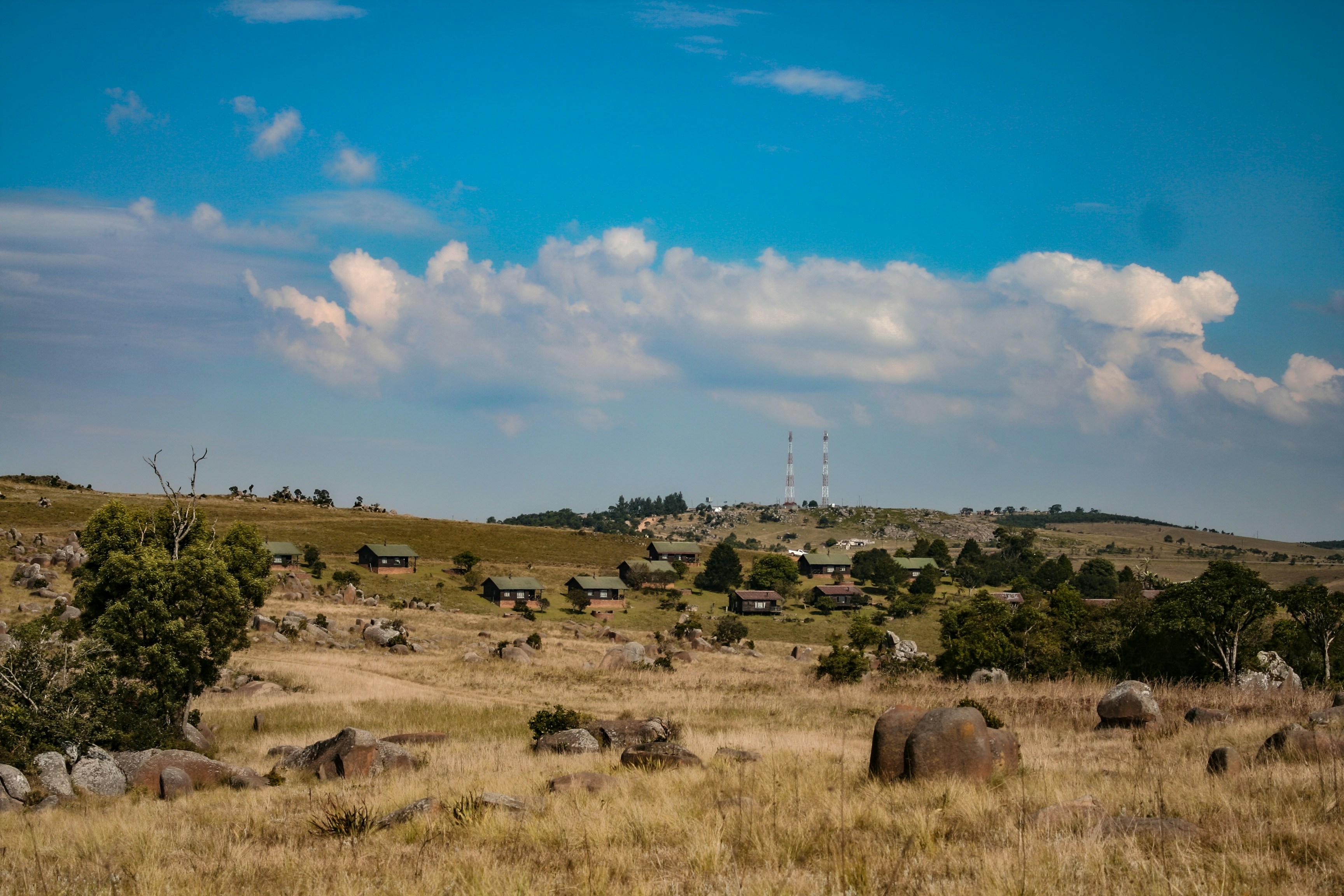 Rolling hills dotted with rustic cabins and rocky formations under a vibrant blue sky with scattered clouds.