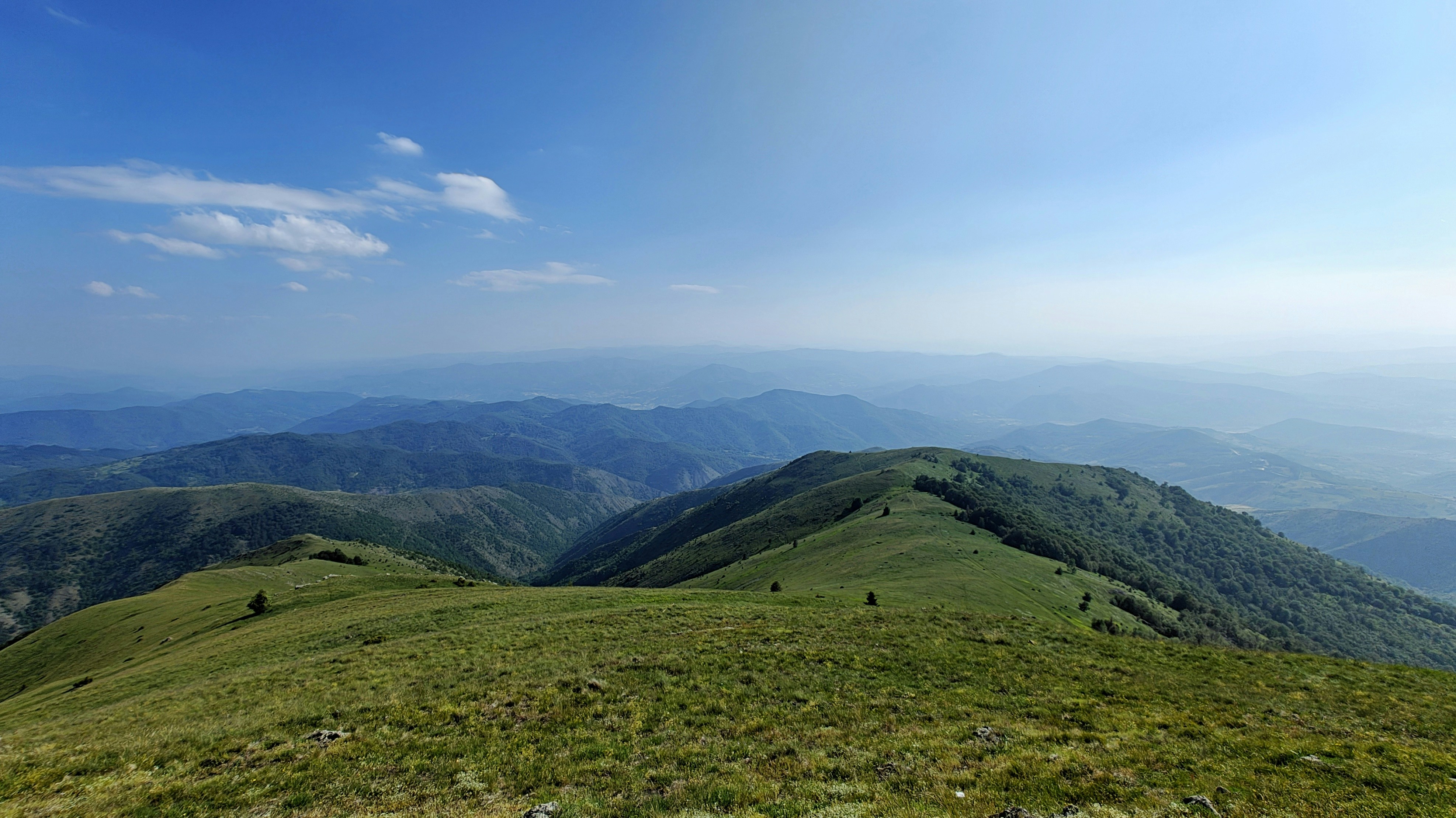 Expansive view of undulating green hills under a clear blue sky, showcasing the serene beauty of nature's landscape.