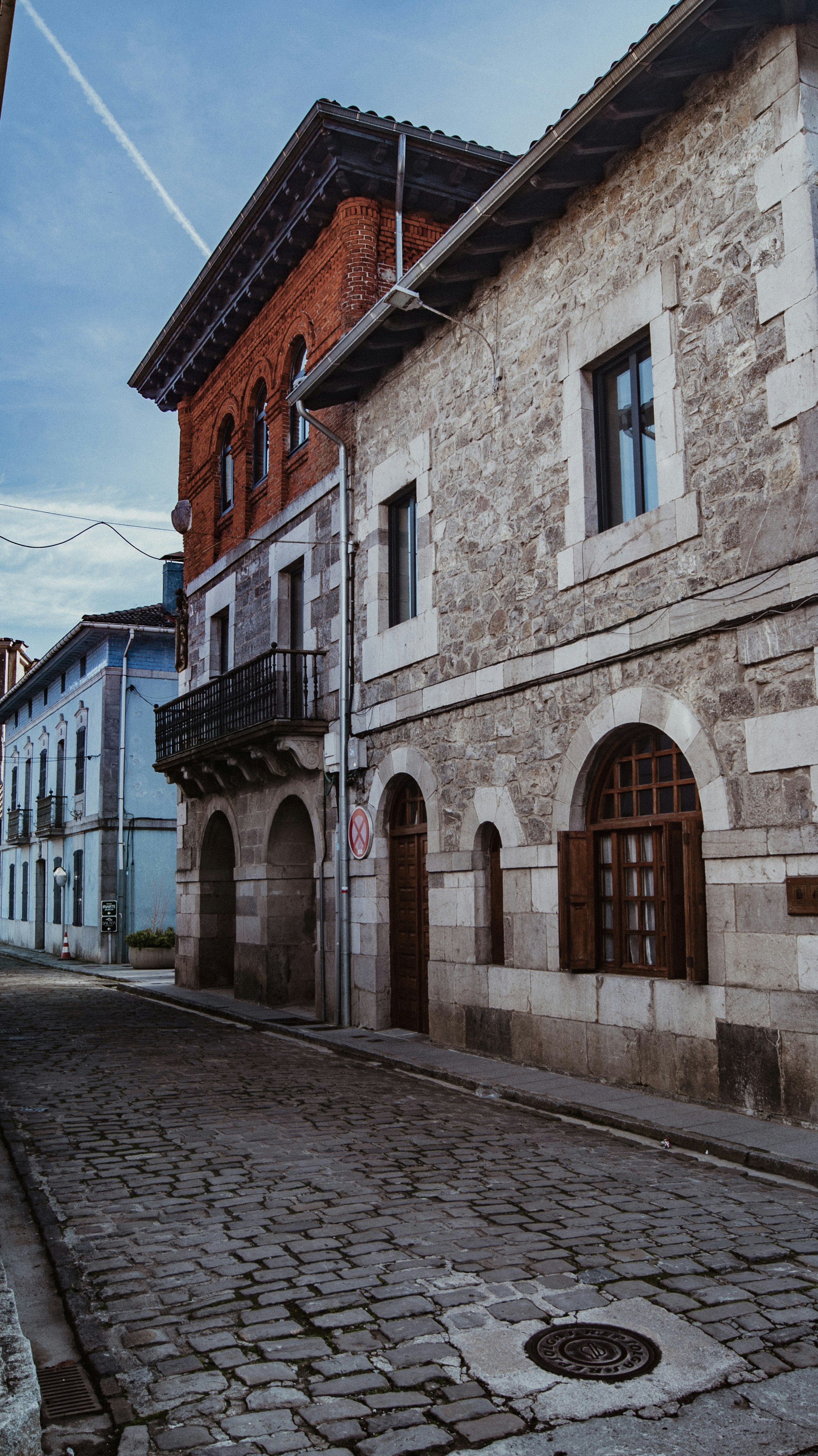 Charming street scene featuring a mix of historical architecture with stone and brick facades, accented by a clear sky. The cobblestone path adds to the vintage ambiance.