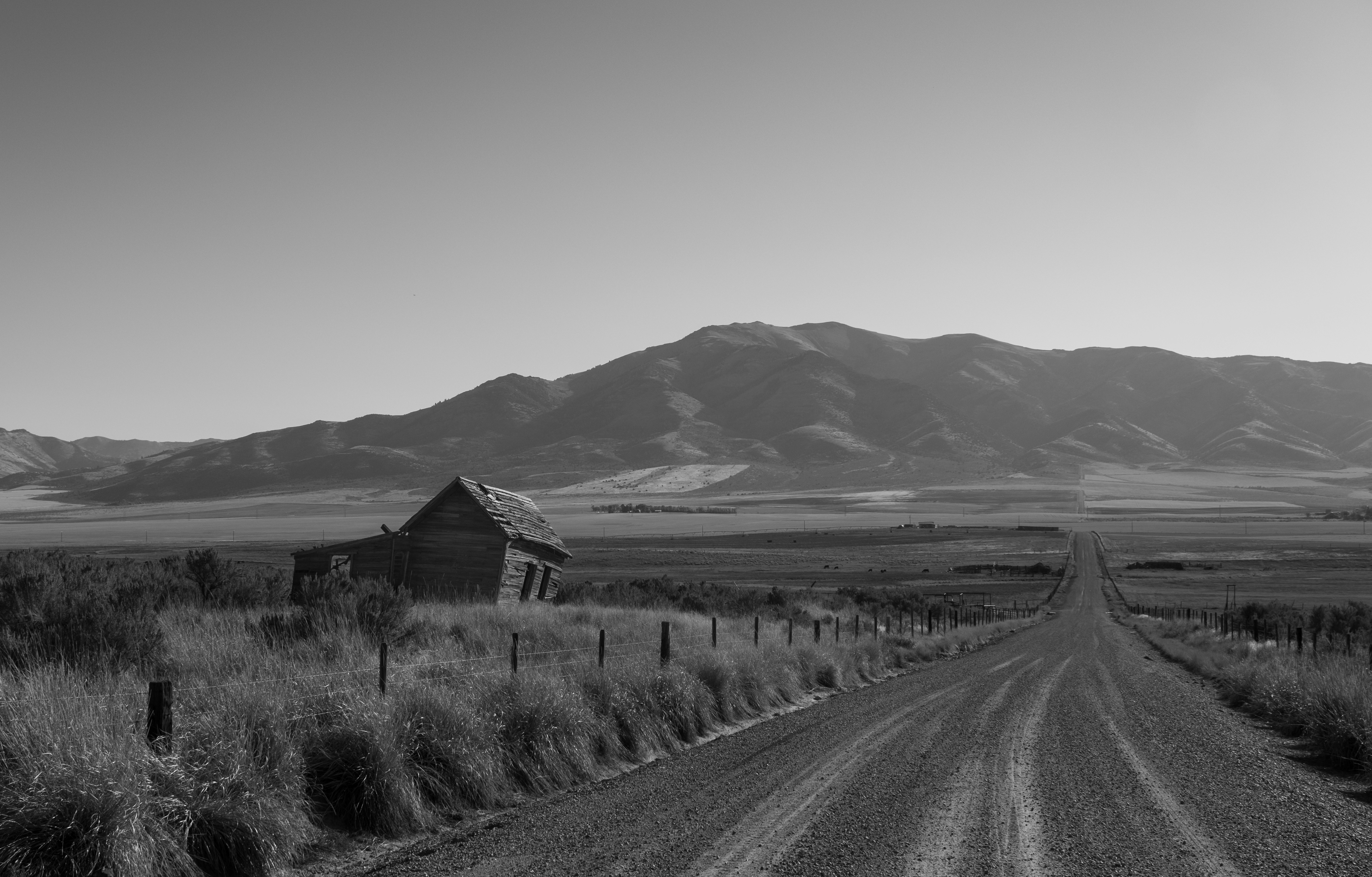 Black and white photograph of a solitary abandoned farm house on a dirt road in Arbon Valley, Idaho, USA, September 29, 2024. | An old building sits along a long, lonely road.