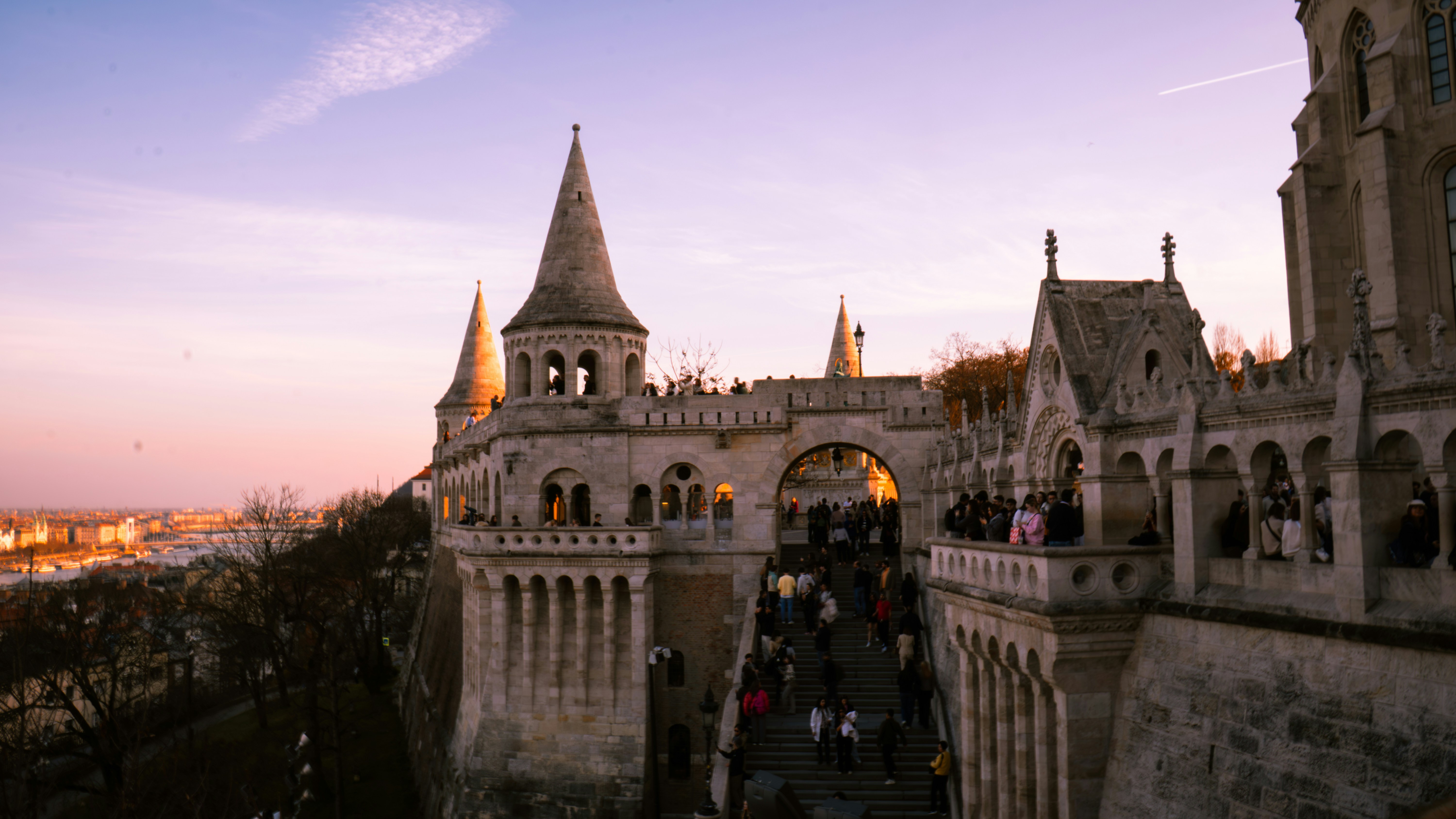 Historic architecture of Fisherman's Bastion illuminated by the soft glow of sunset, with visitors enjoying the view. 