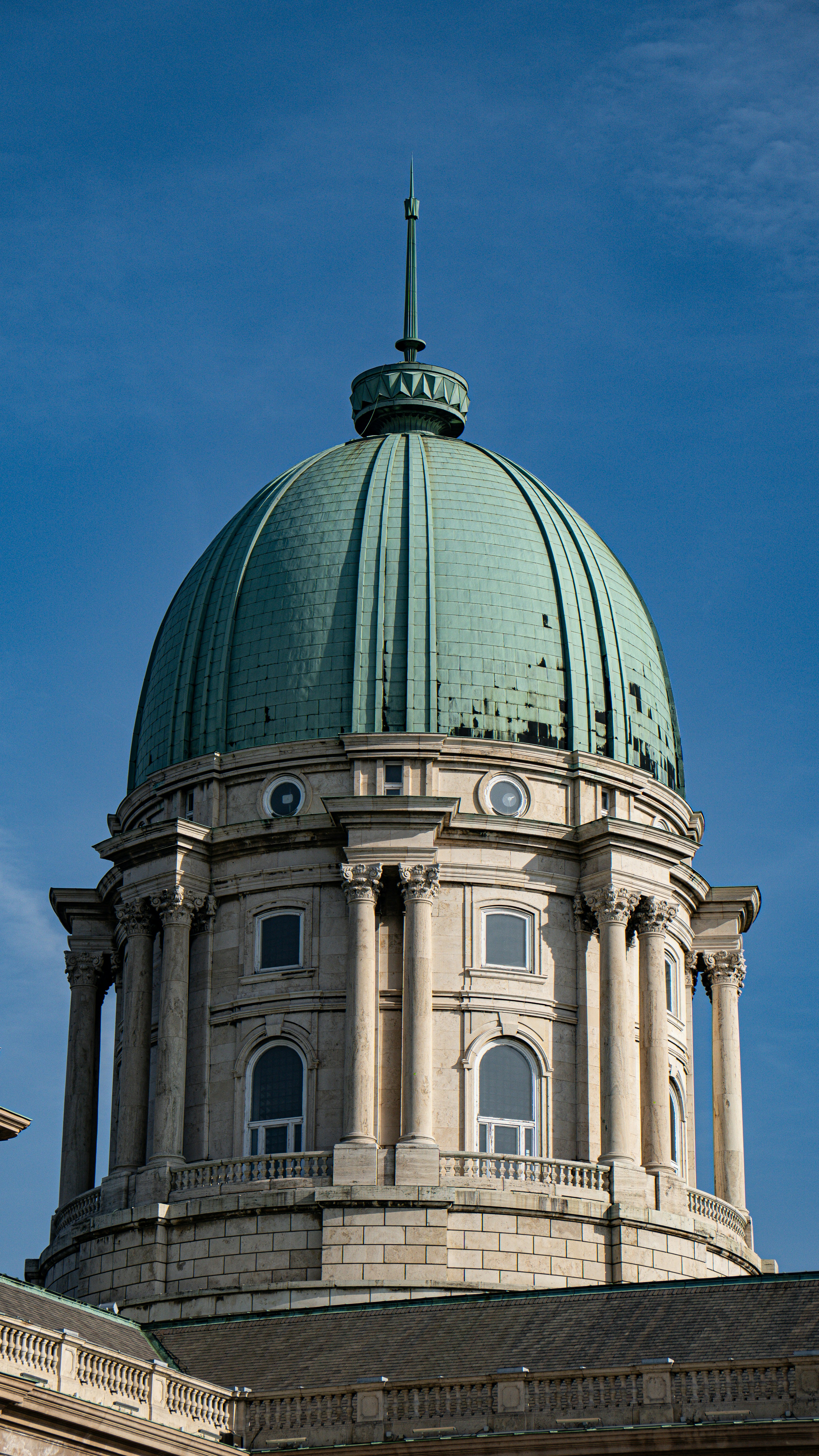 Architectural dome with a weathered green patina, showcasing intricate details against a clear blue sky.