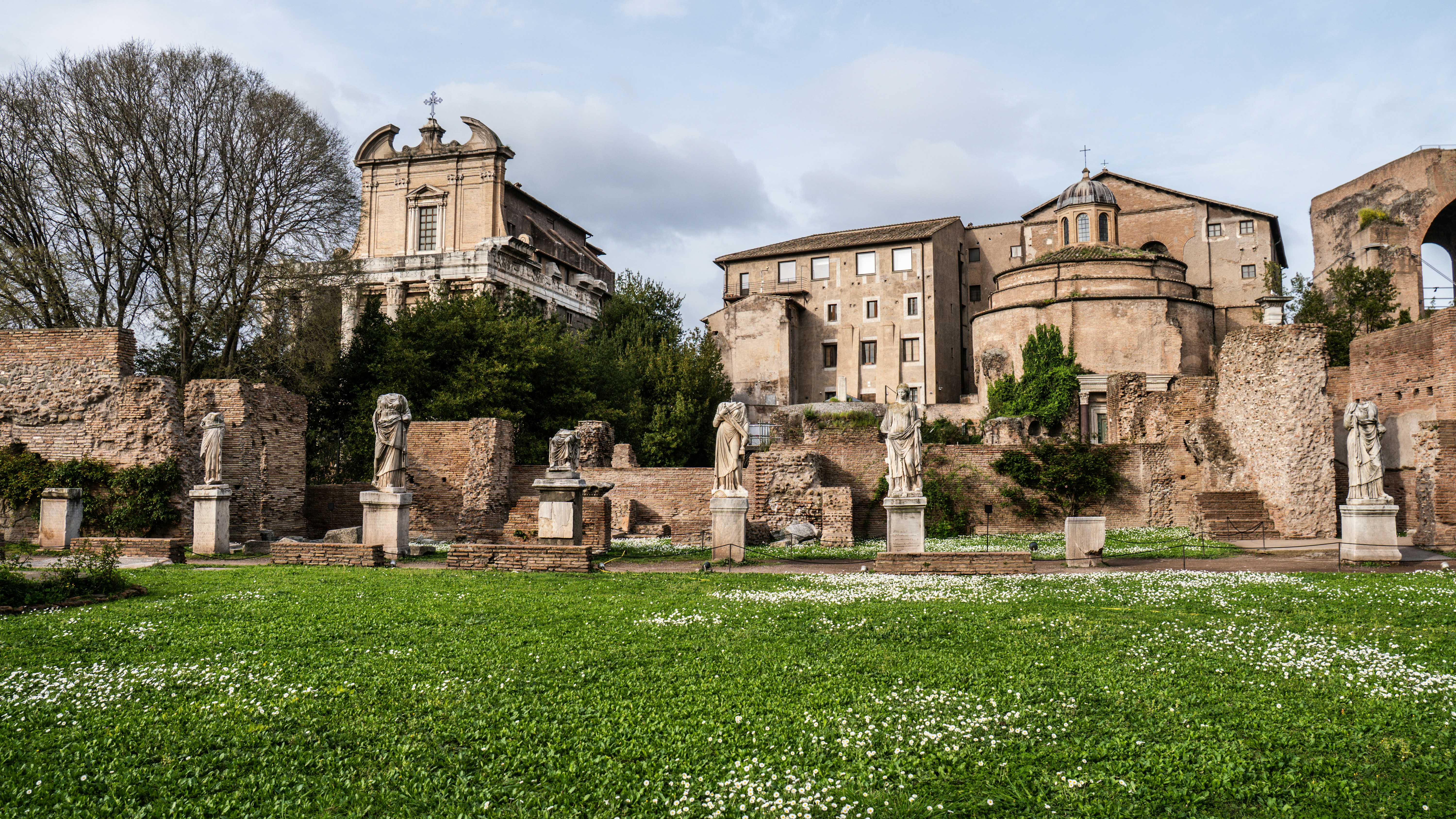 Ancient statues stand amidst lush greenery and historical architecture, showcasing the remnants of Roman civilization.