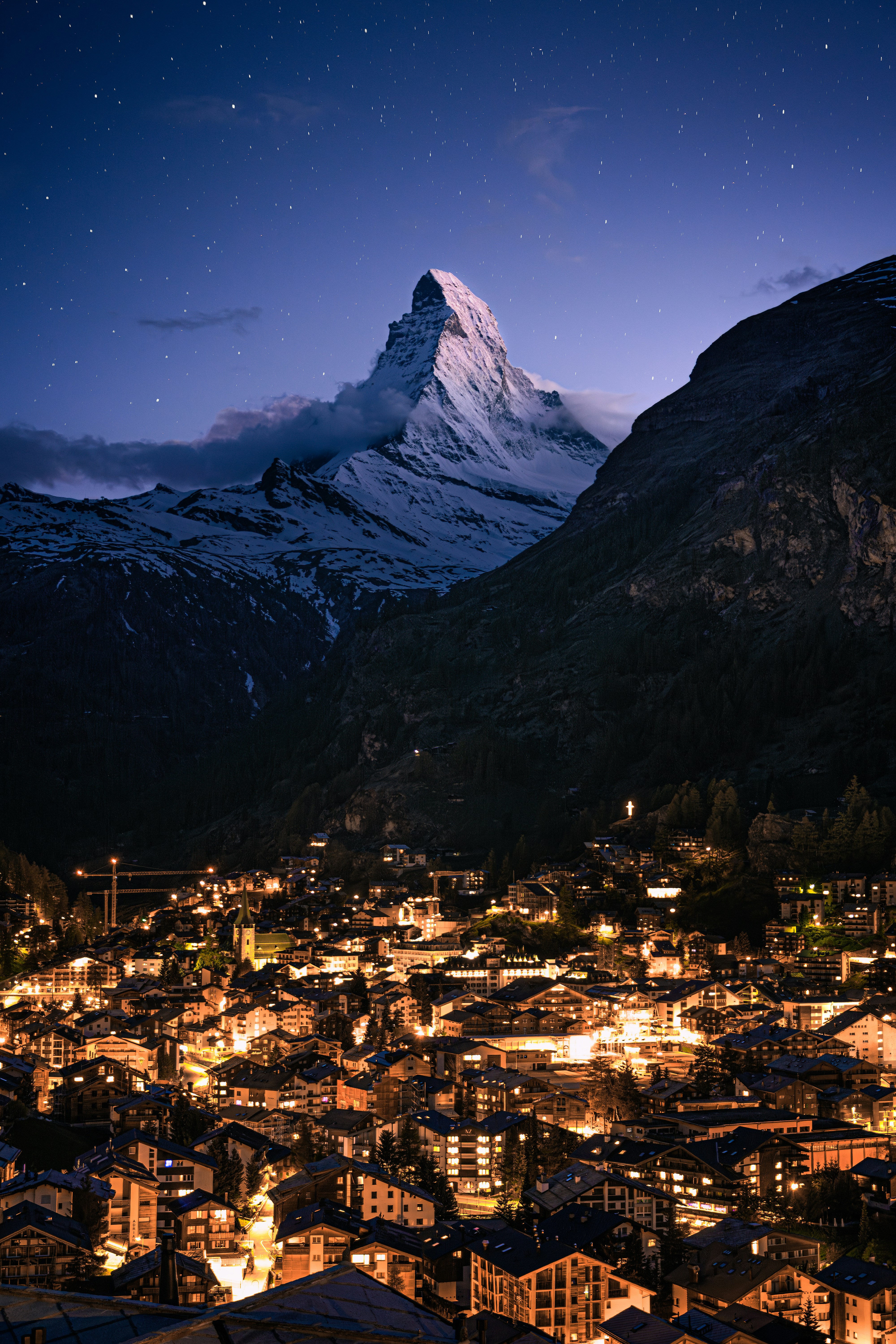 Zermatt under the starry sky with the Matterhorn in the background. | Night view of a town under a starry mountain.
