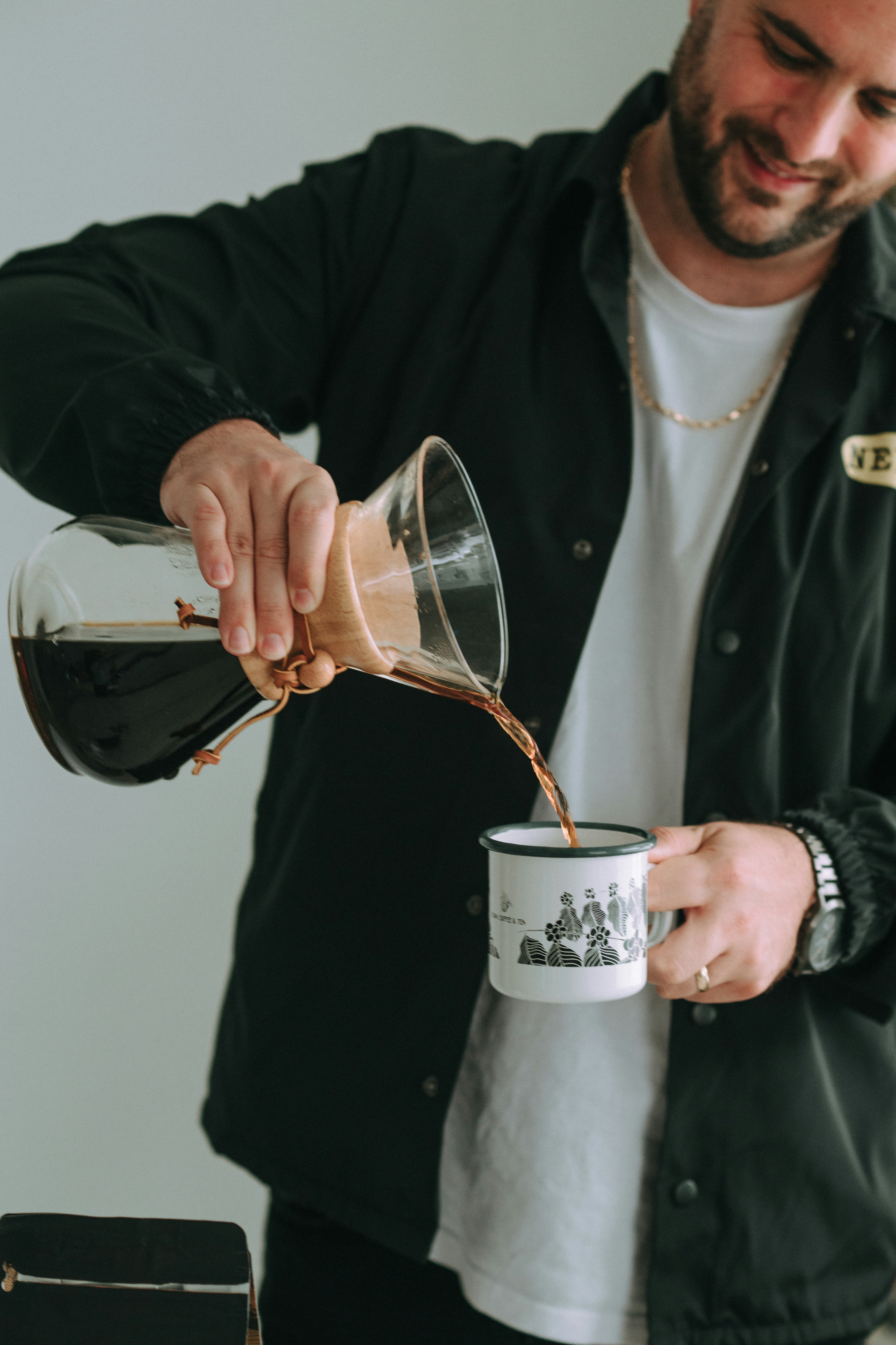 Barista pouring freshly brewed coffee from a glass carafe into a patterned mug, highlighting the art of coffee preparation.