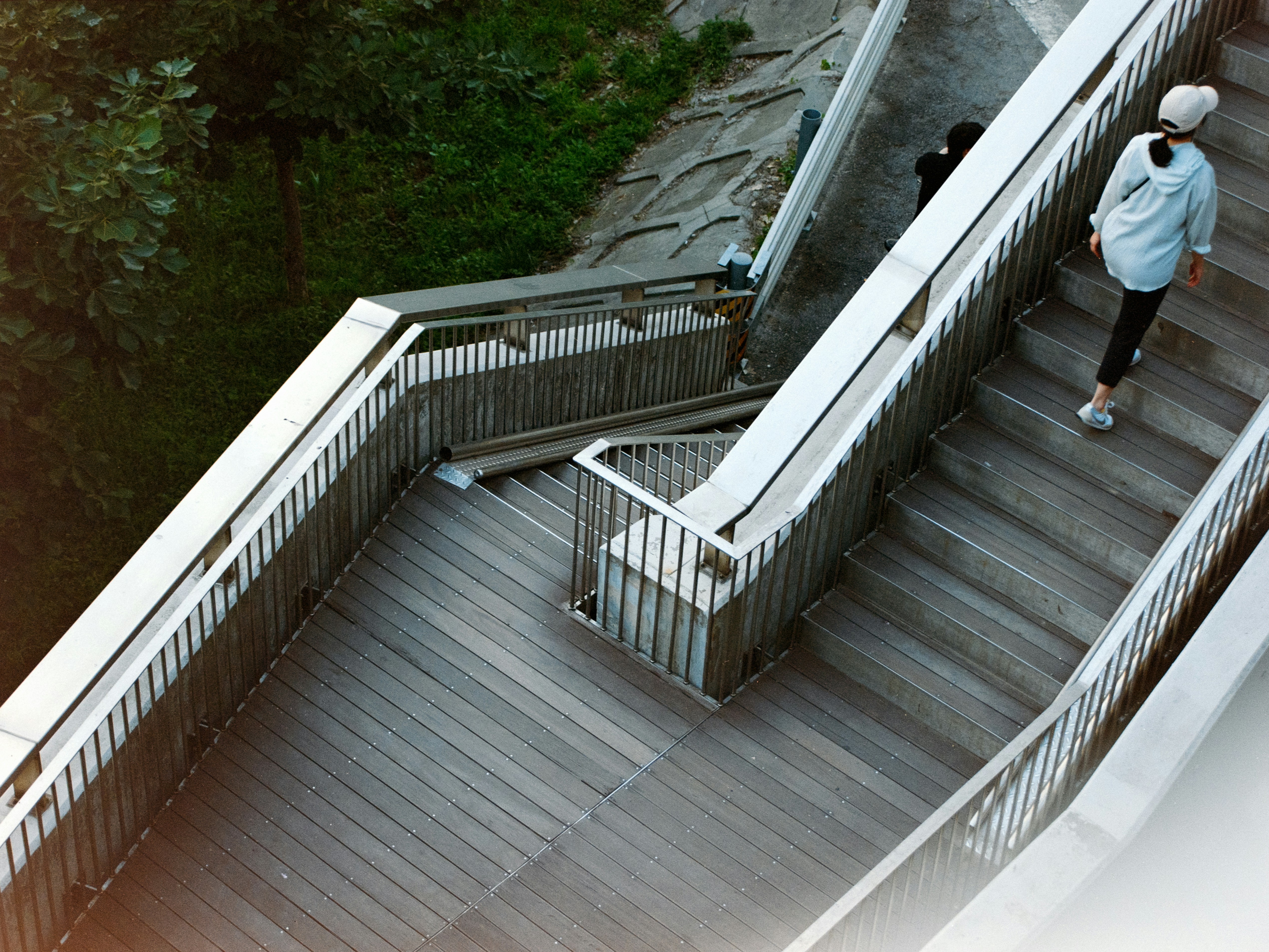 A person navigates a wooden staircase in an urban setting, surrounded by greenery and modern architecture.