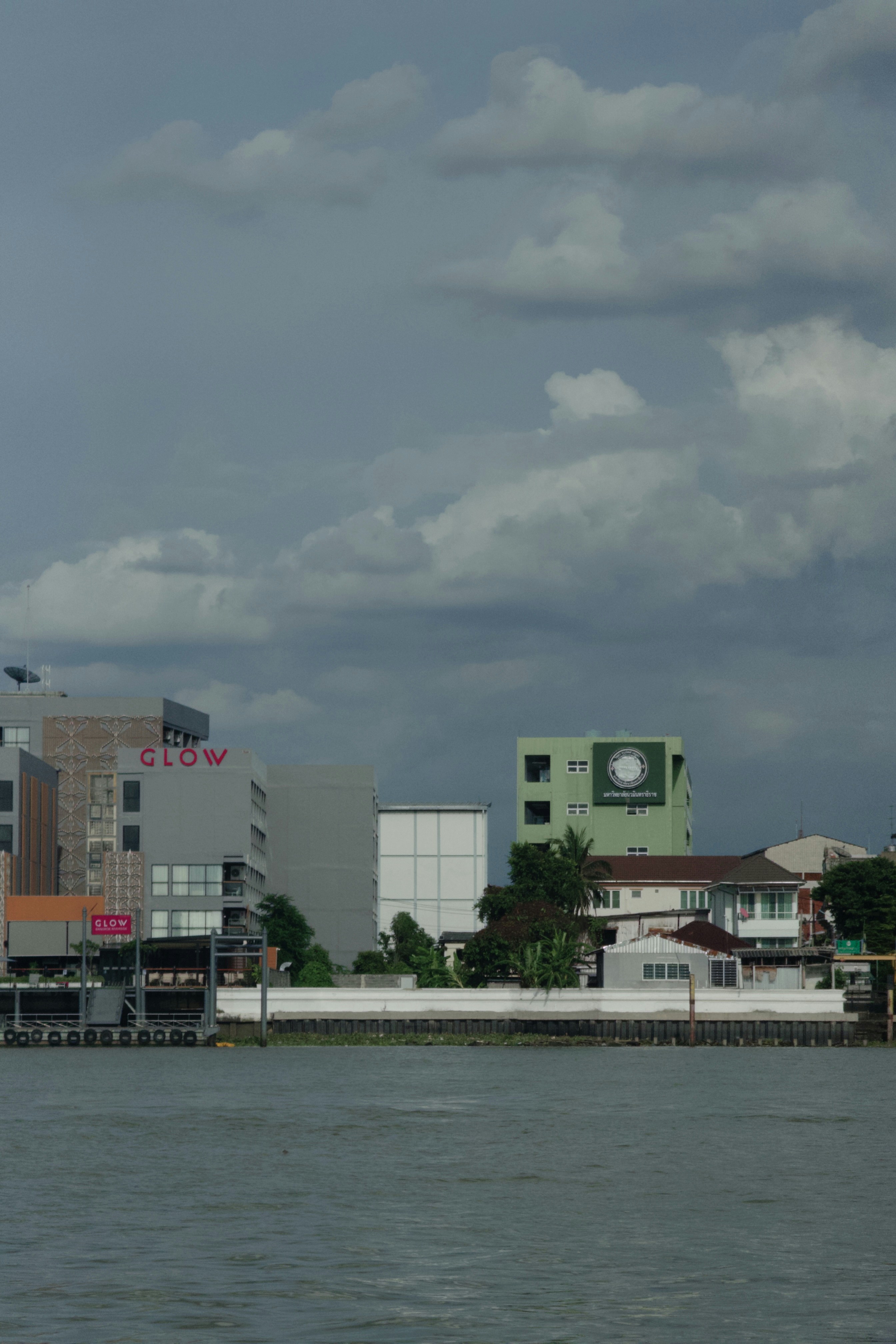Buildings line a river under a cloudy sky.
