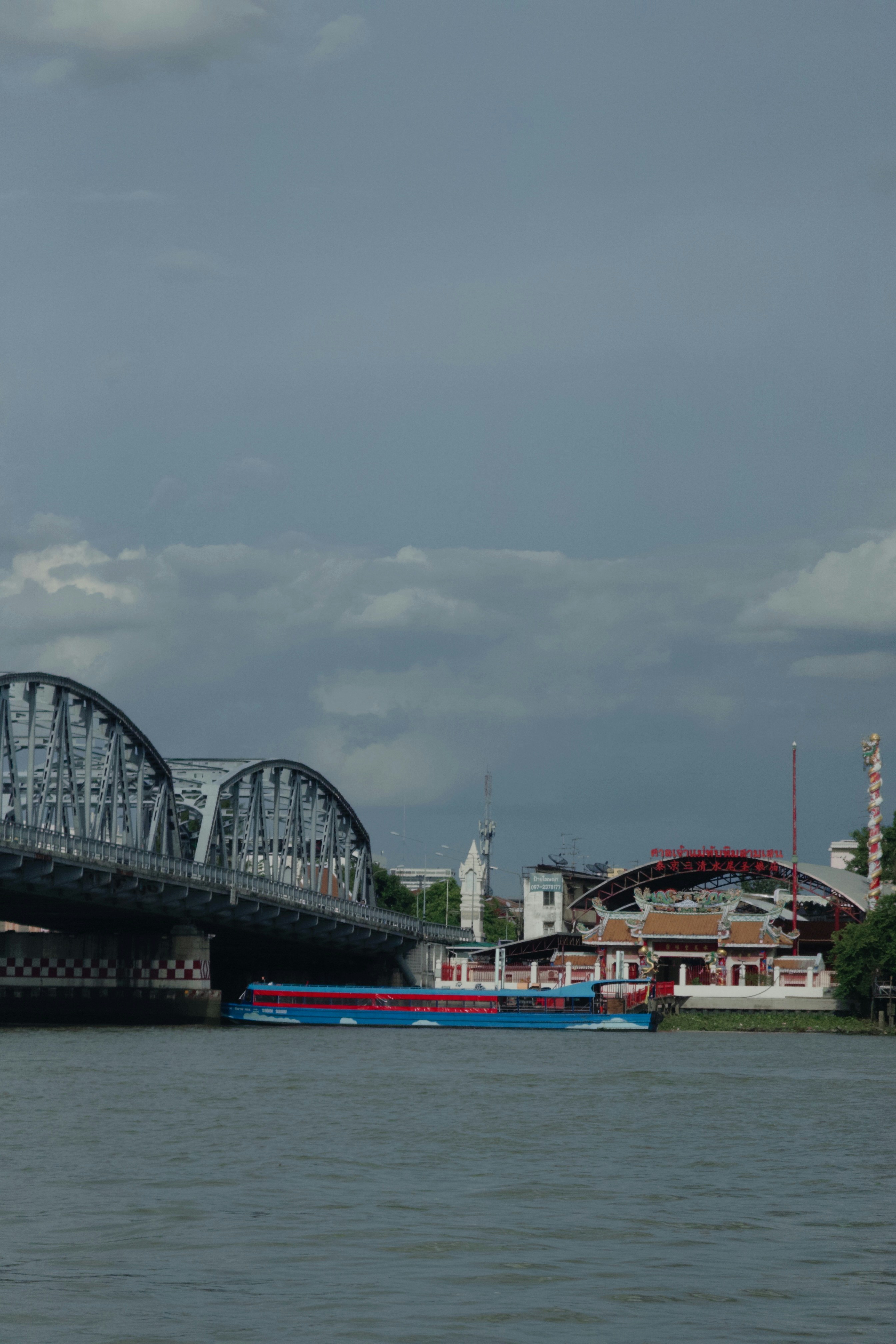 Bridge and buildings along a river under cloudy skies.