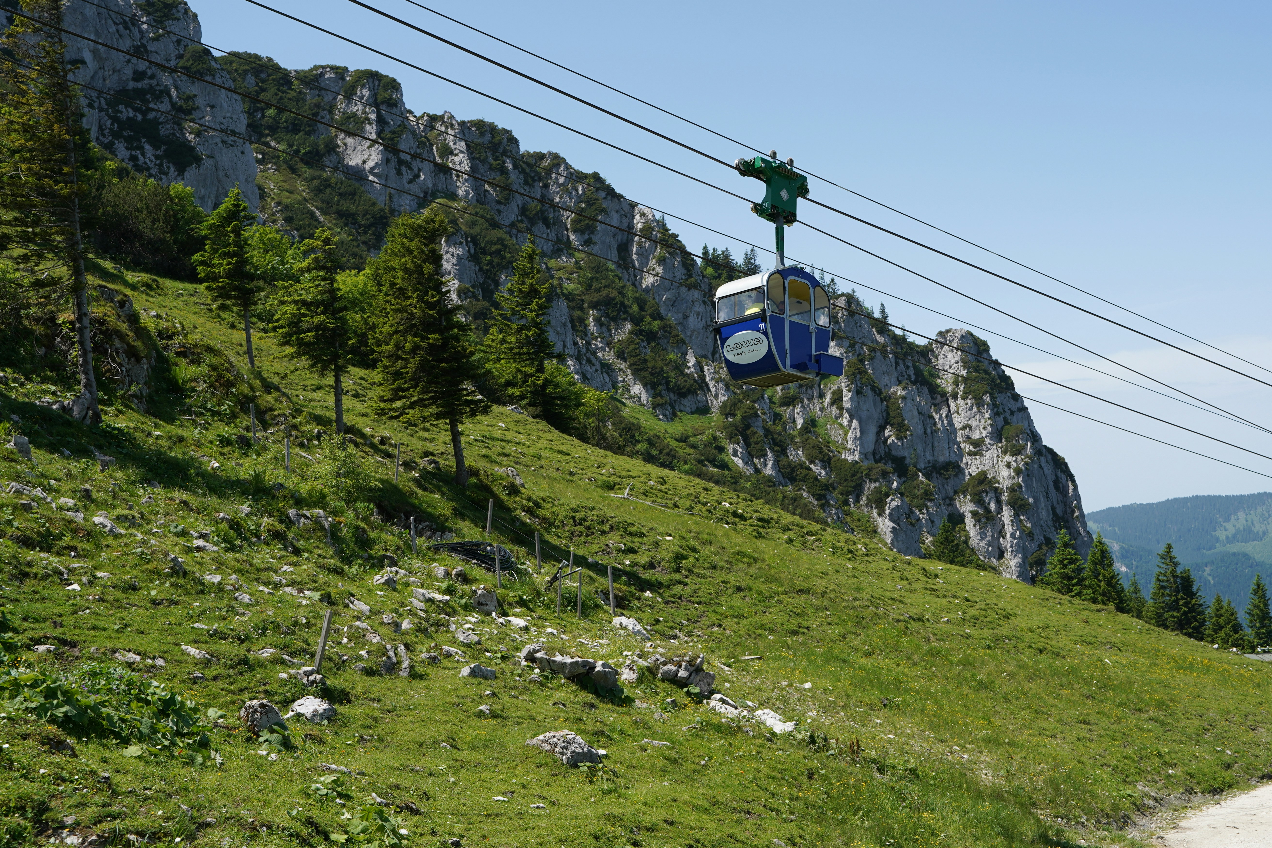 A vibrant cable car gliding through lush green hills under a clear blue sky, showcasing the beauty of mountain landscapes.