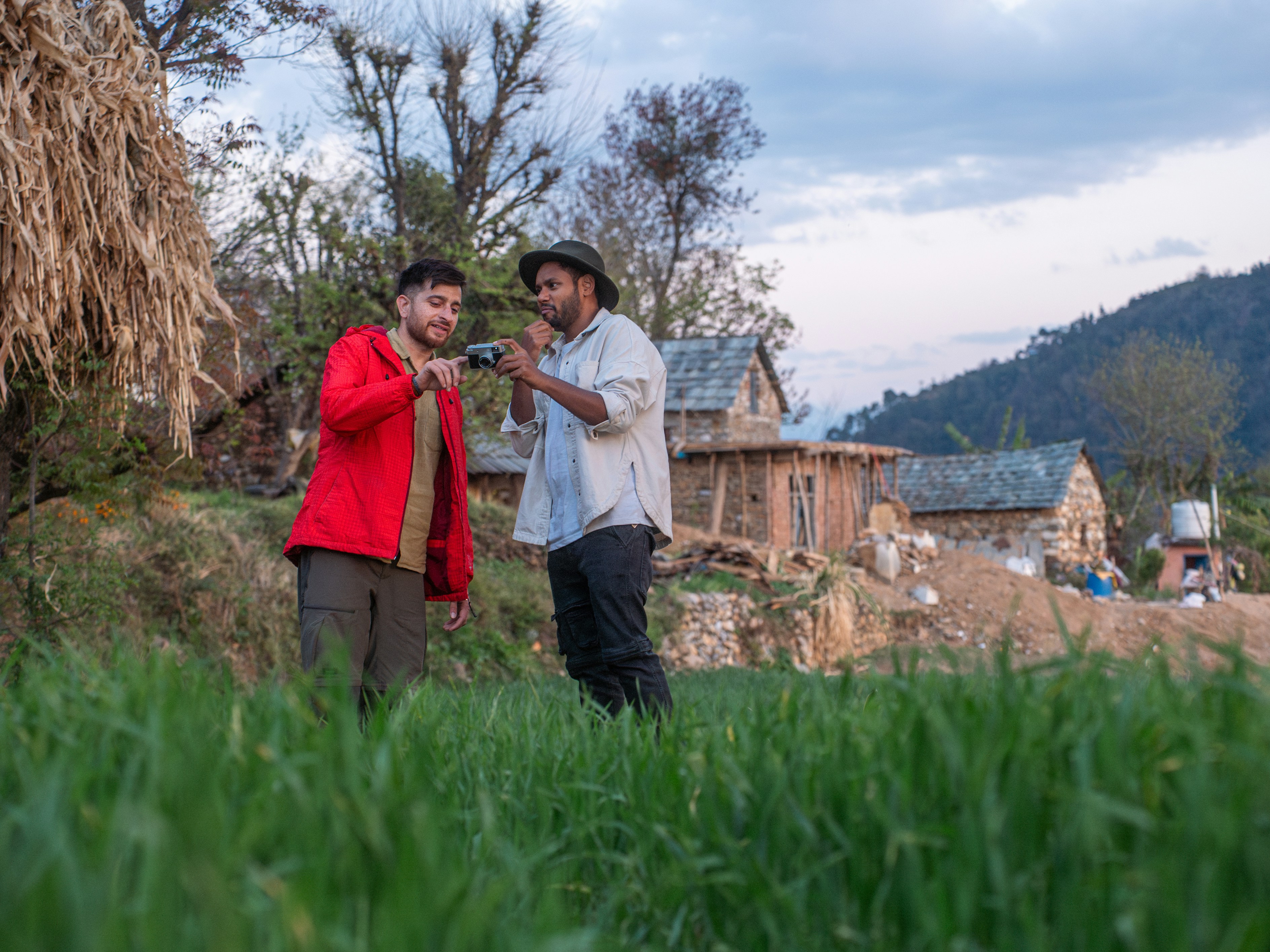 Two friends in a rural village sharing a moment with a smoke or gadget near a thatched hut