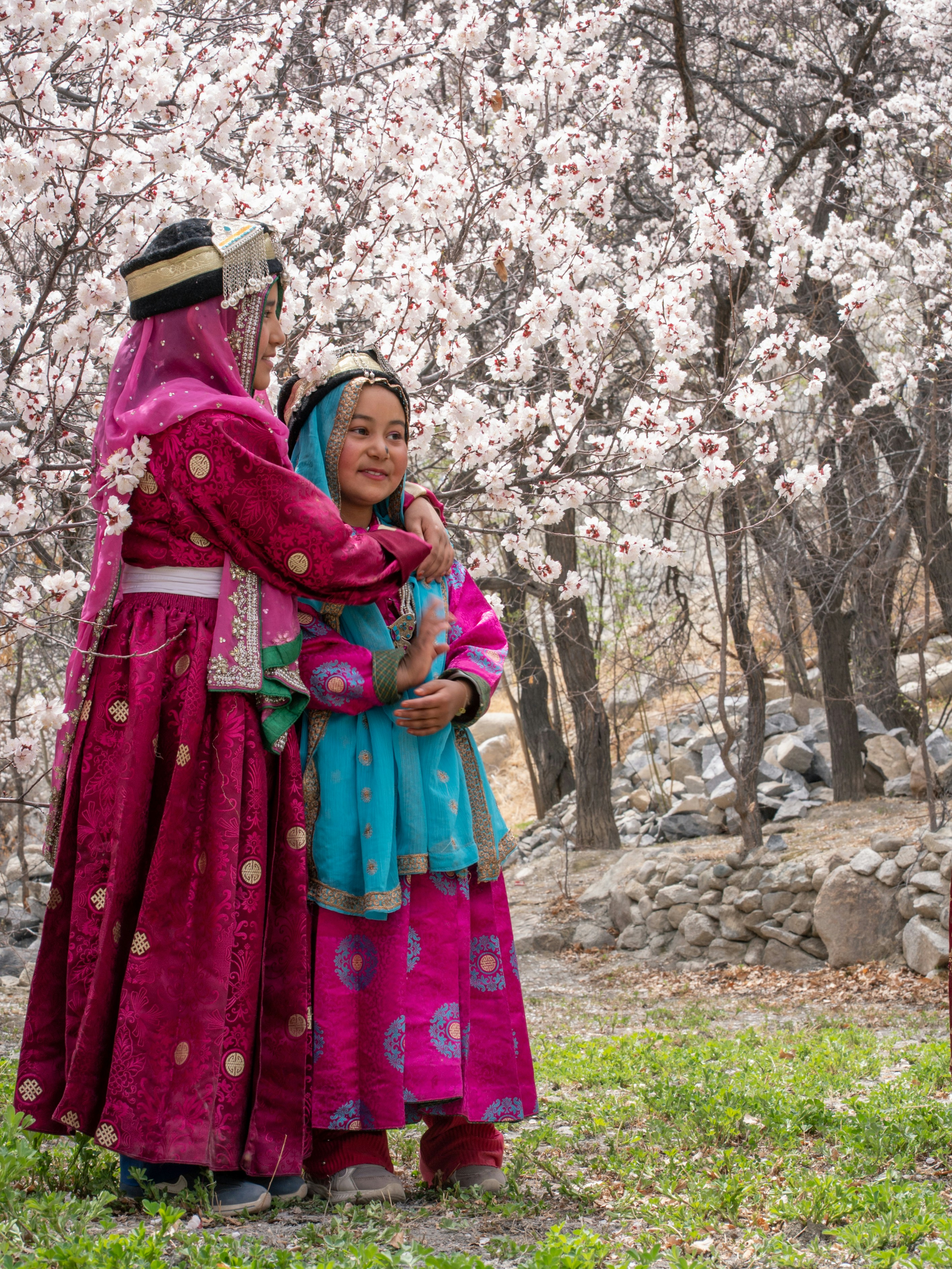Two girls in traditional clothes pose with blossoming trees.