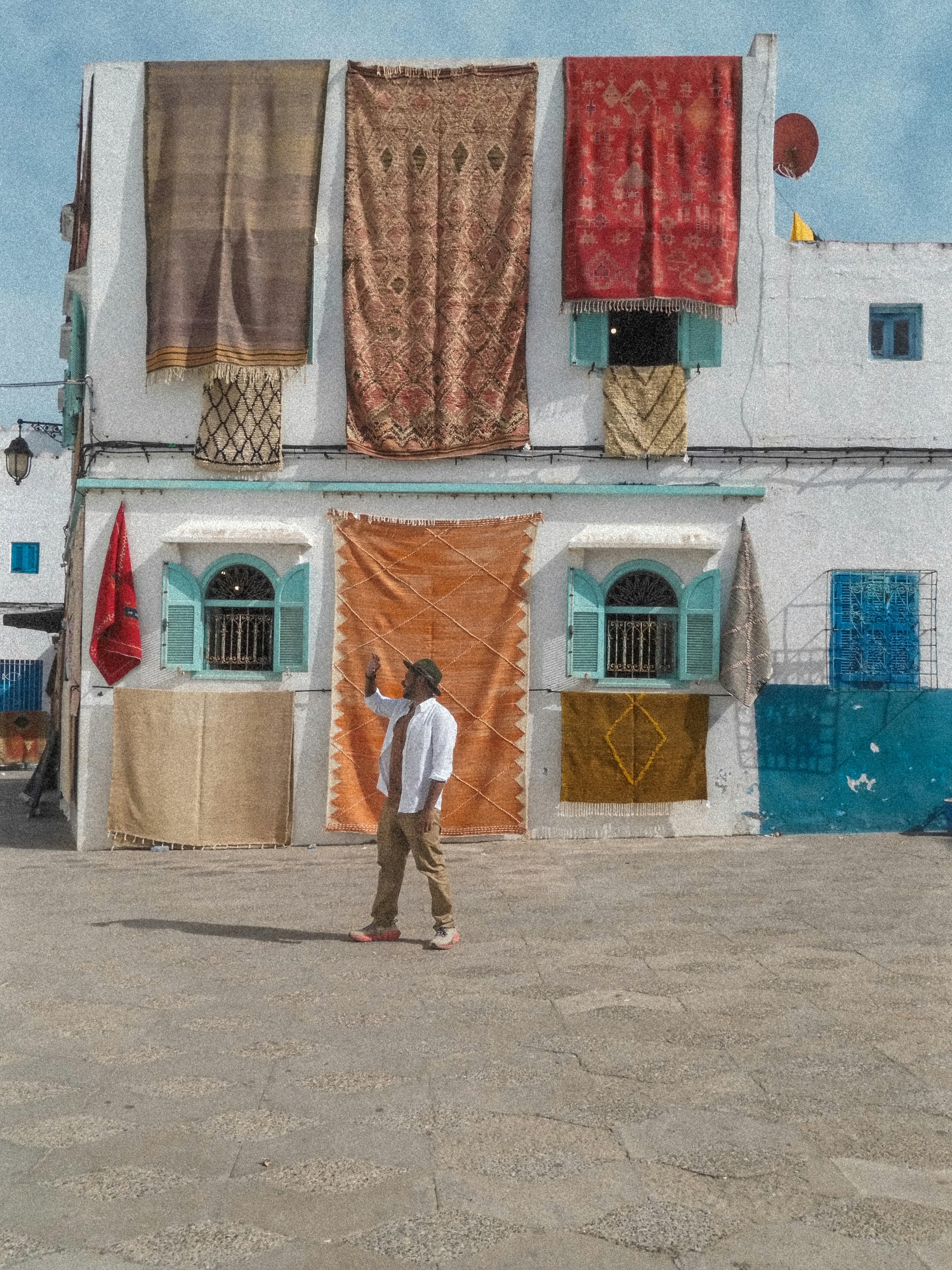 A man gestures in front of a vibrant building adorned with colorful textiles and intricate patterns, showcasing local craftsmanship and culture.